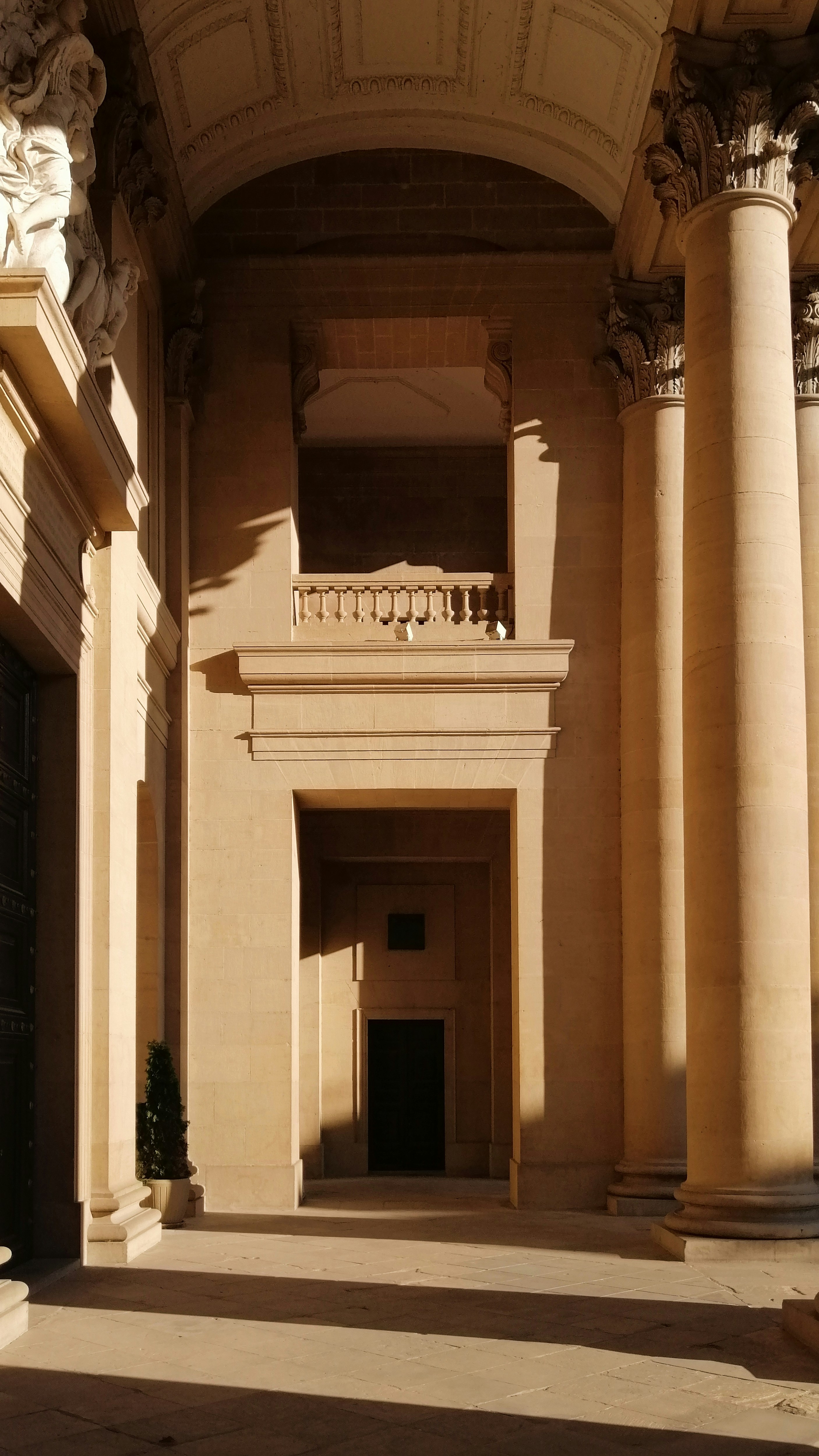Elegant columns and intricate details frame a shadowed doorway in a grand architectural setting.