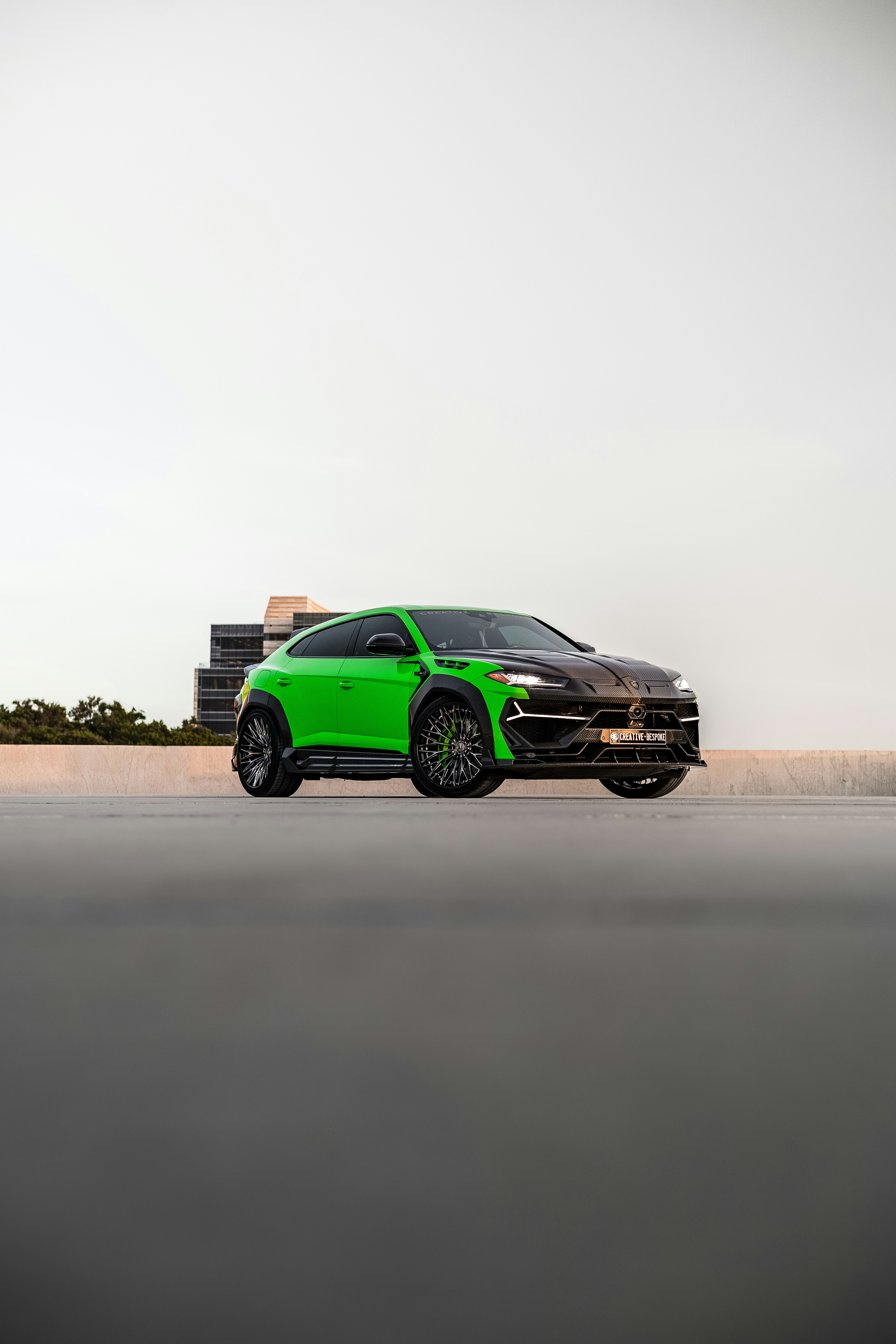 A striking dual-tone car featuring a black and bright green exterior, parked on a sleek urban rooftop. The modern city skyline serves as a backdrop.