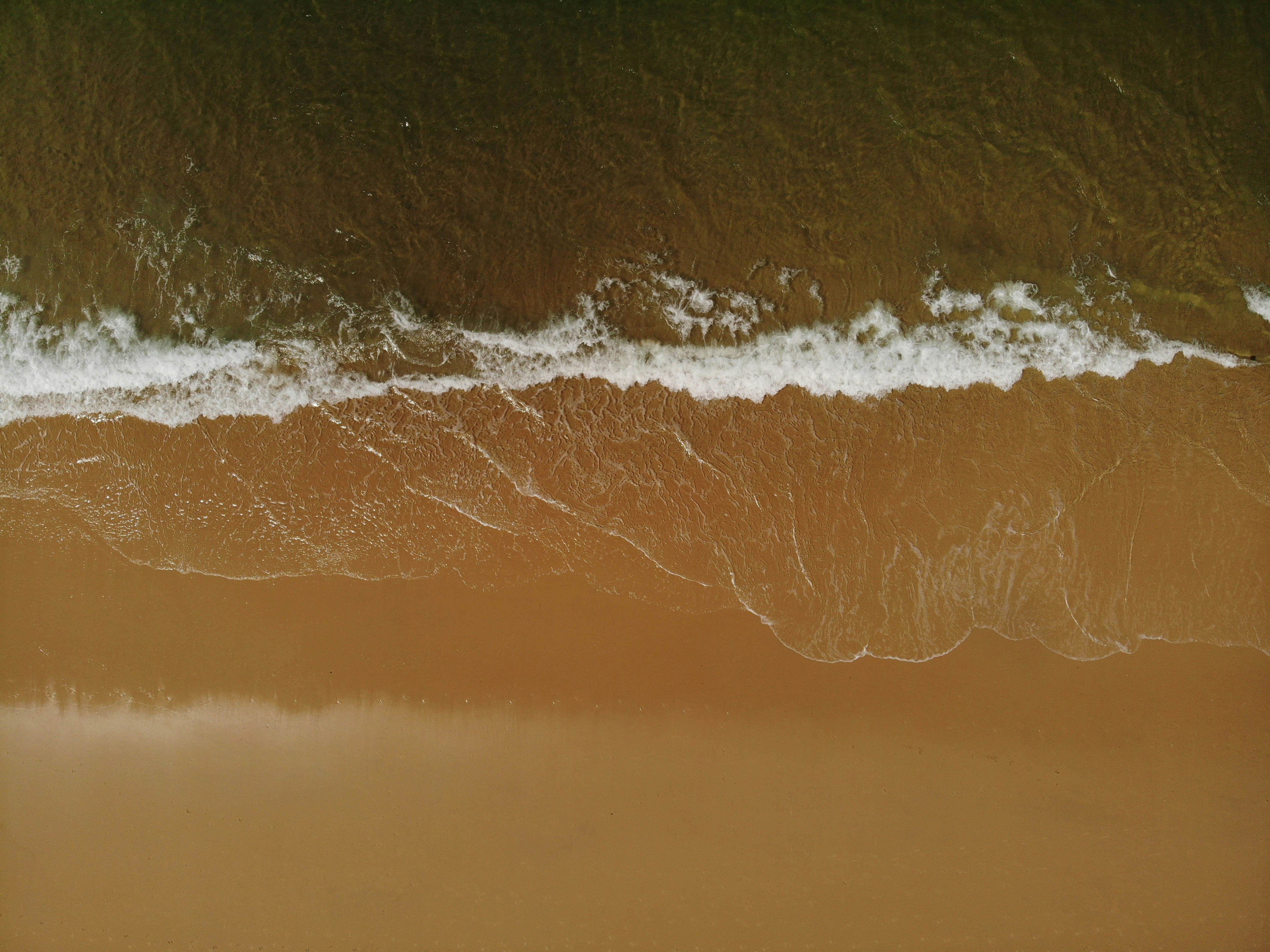 Aerial view capturing the gentle meeting of ocean waves and sandy beach, highlighting the dynamic patterns of water and land.