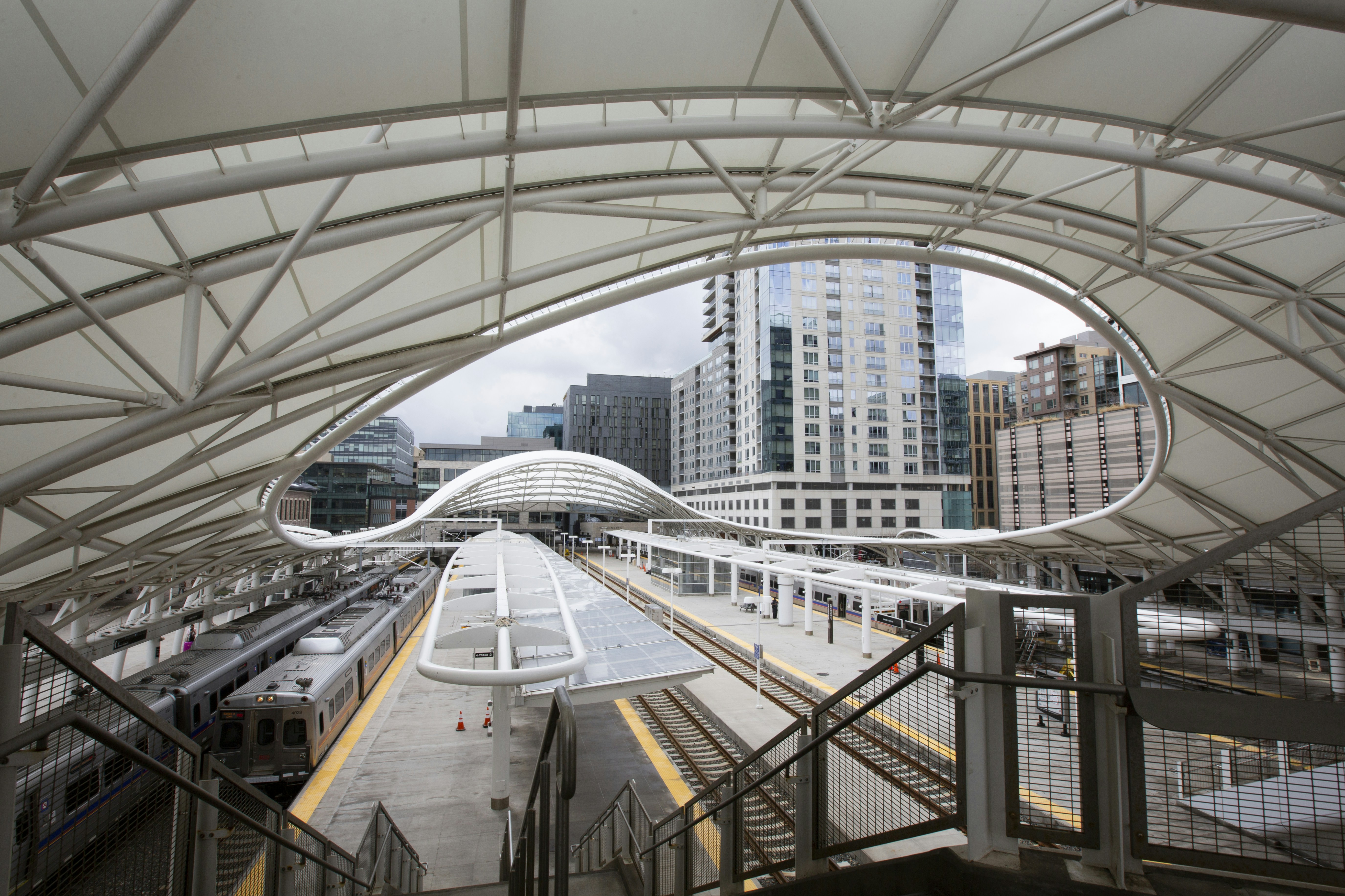 Train station platform framed by an architectural canopy with city buildings in the background.
