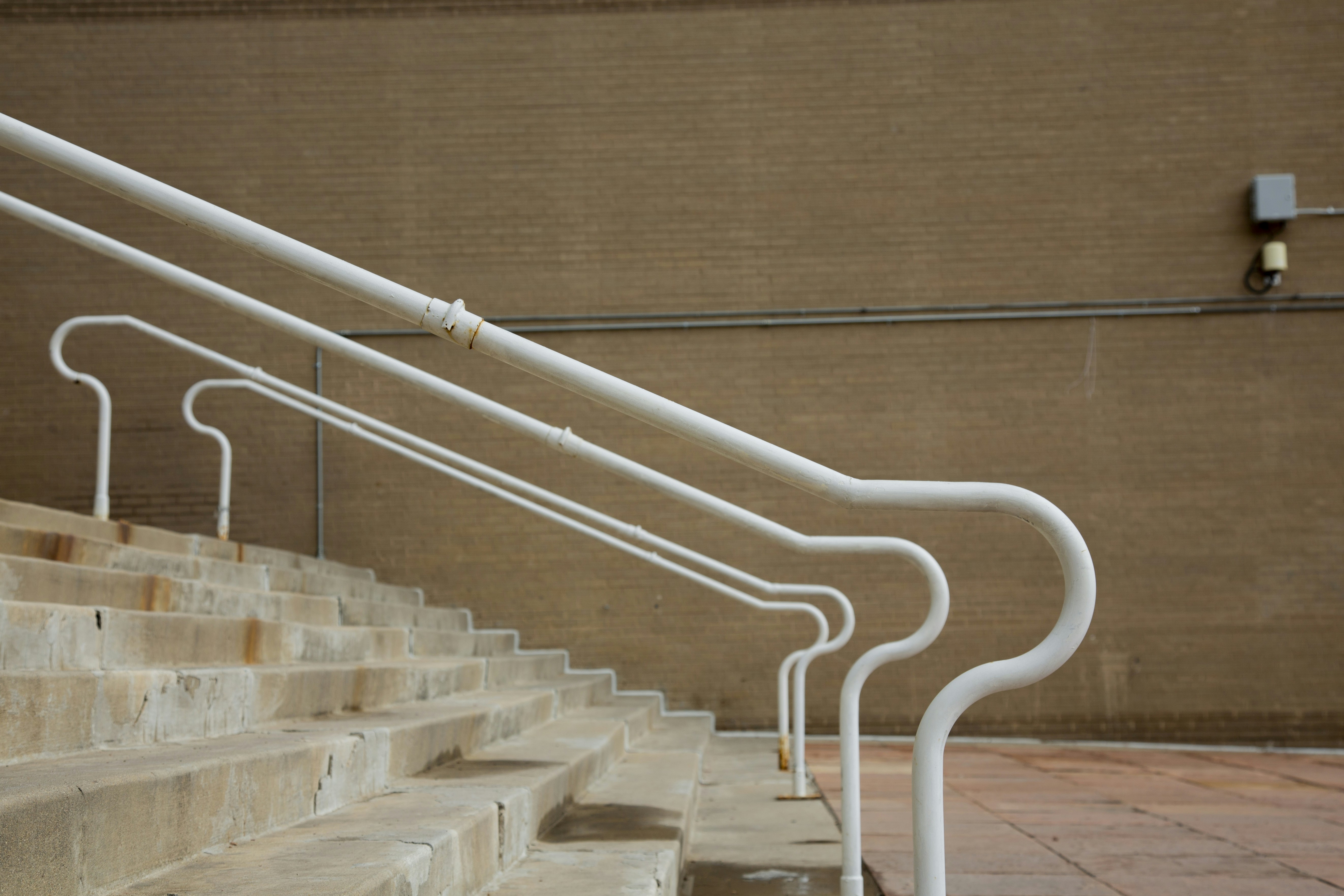 White handrails gracefully curve alongside concrete steps, showcasing modern architectural accessibility features. The textured surface of the steps contrasts with the smooth lines of the railings.