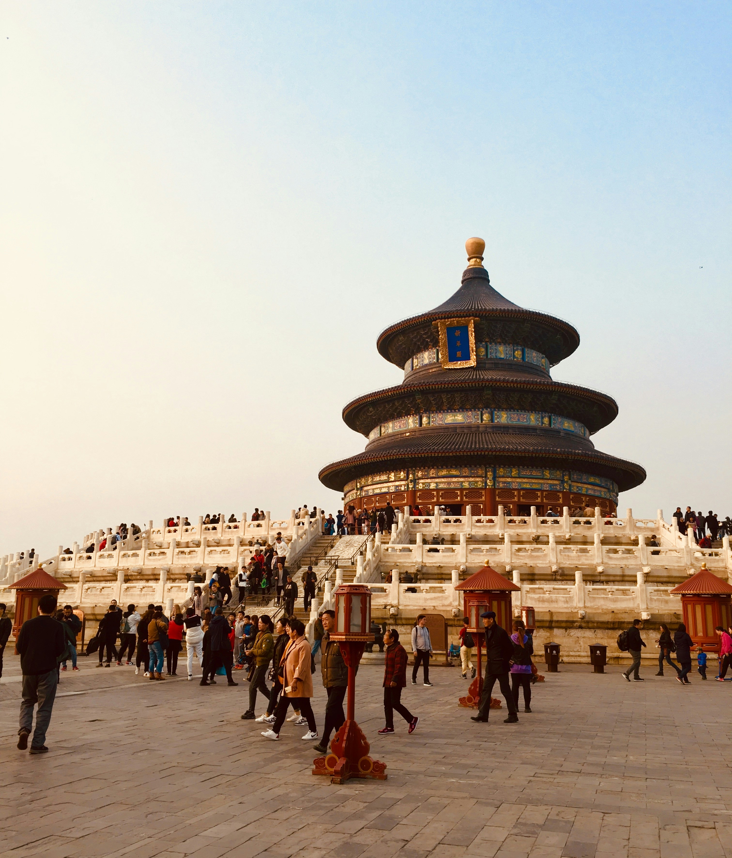 The Temple of Heaven stands majestically against a pale sky, surrounded by visitors exploring its intricate architecture and serene grounds.