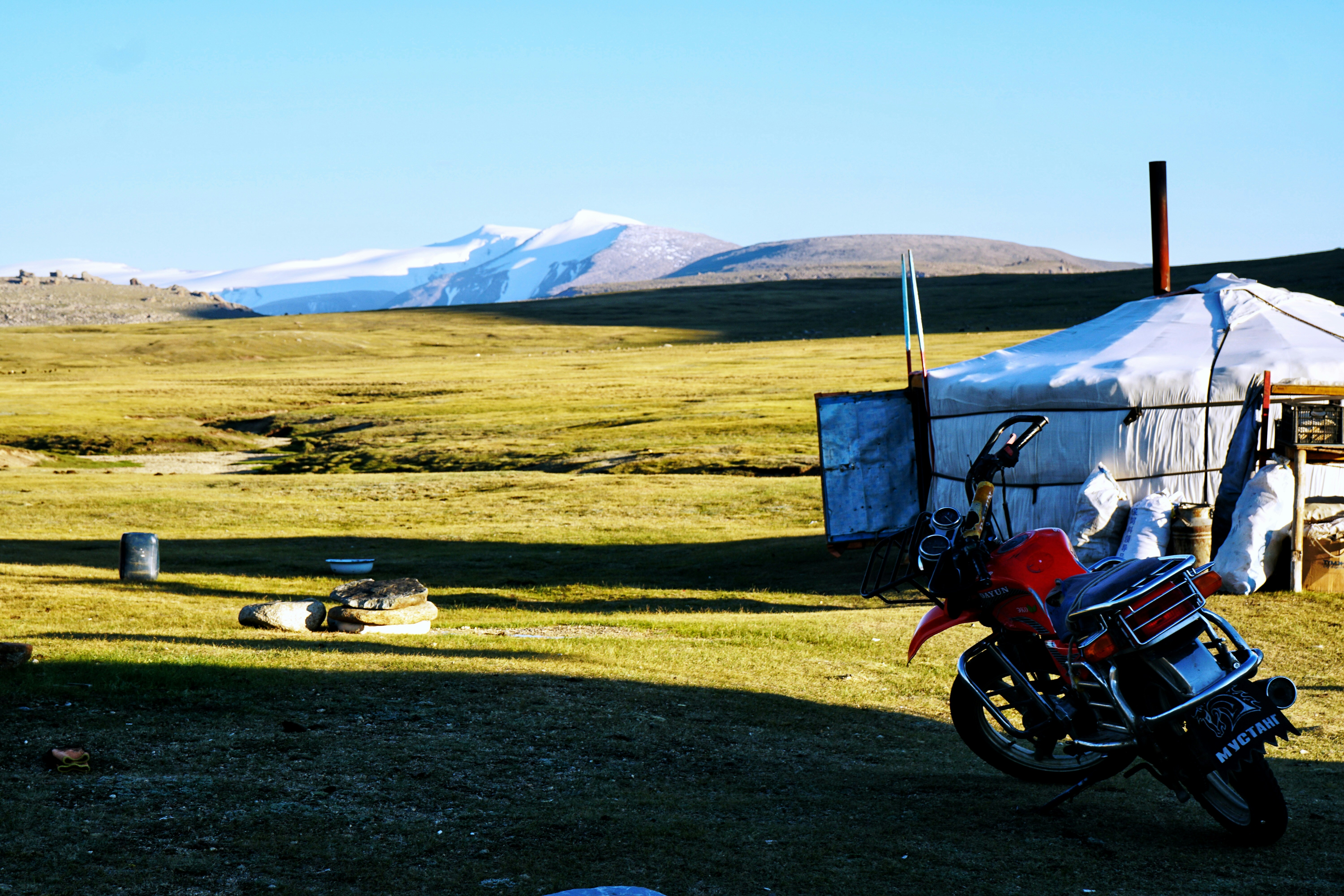 Red Motorcycle Resting by a White Tent as Snow-Capped Peaks Rise in the Distance