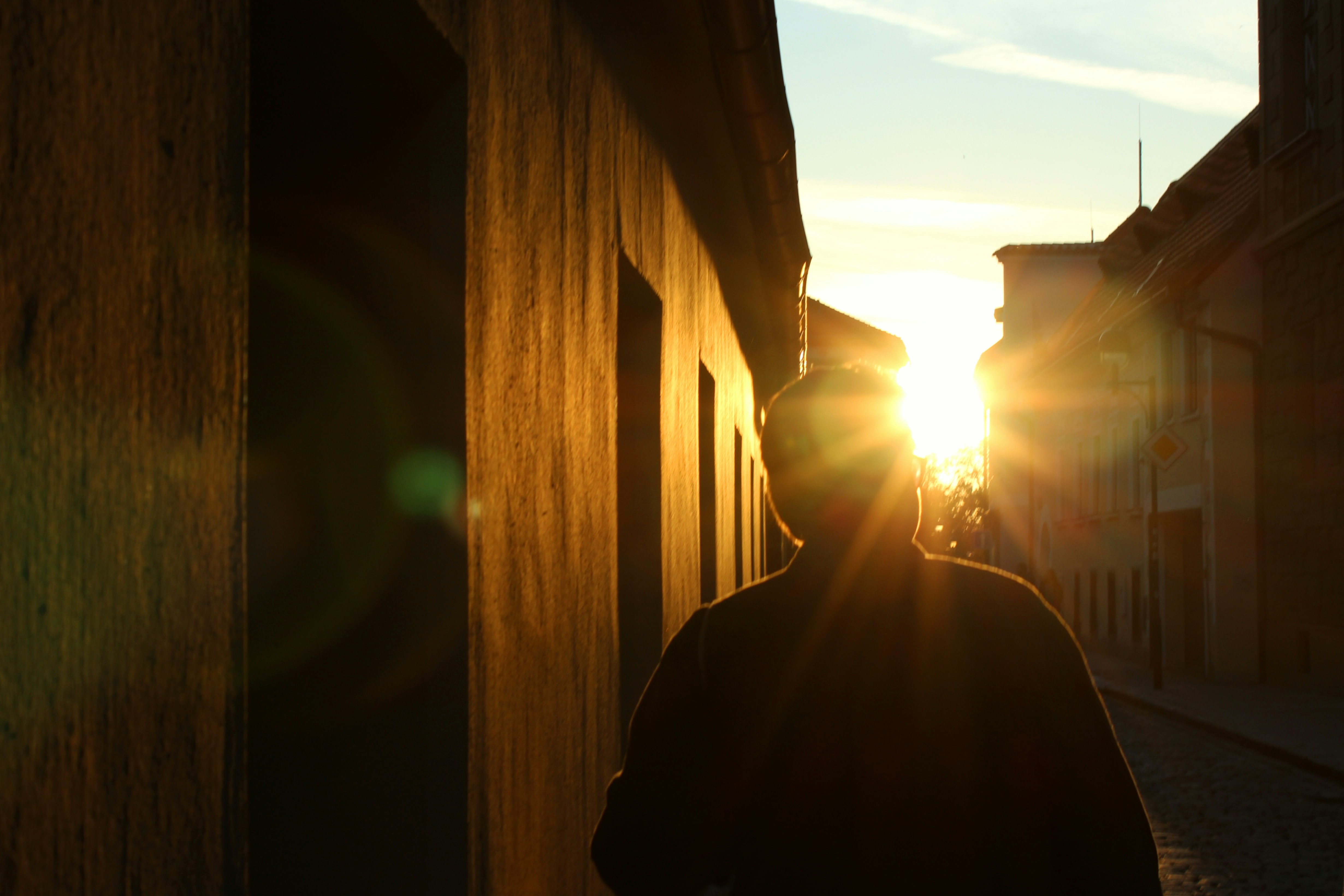 Silhouette of a person walking through a narrow alley with the sun setting behind them.