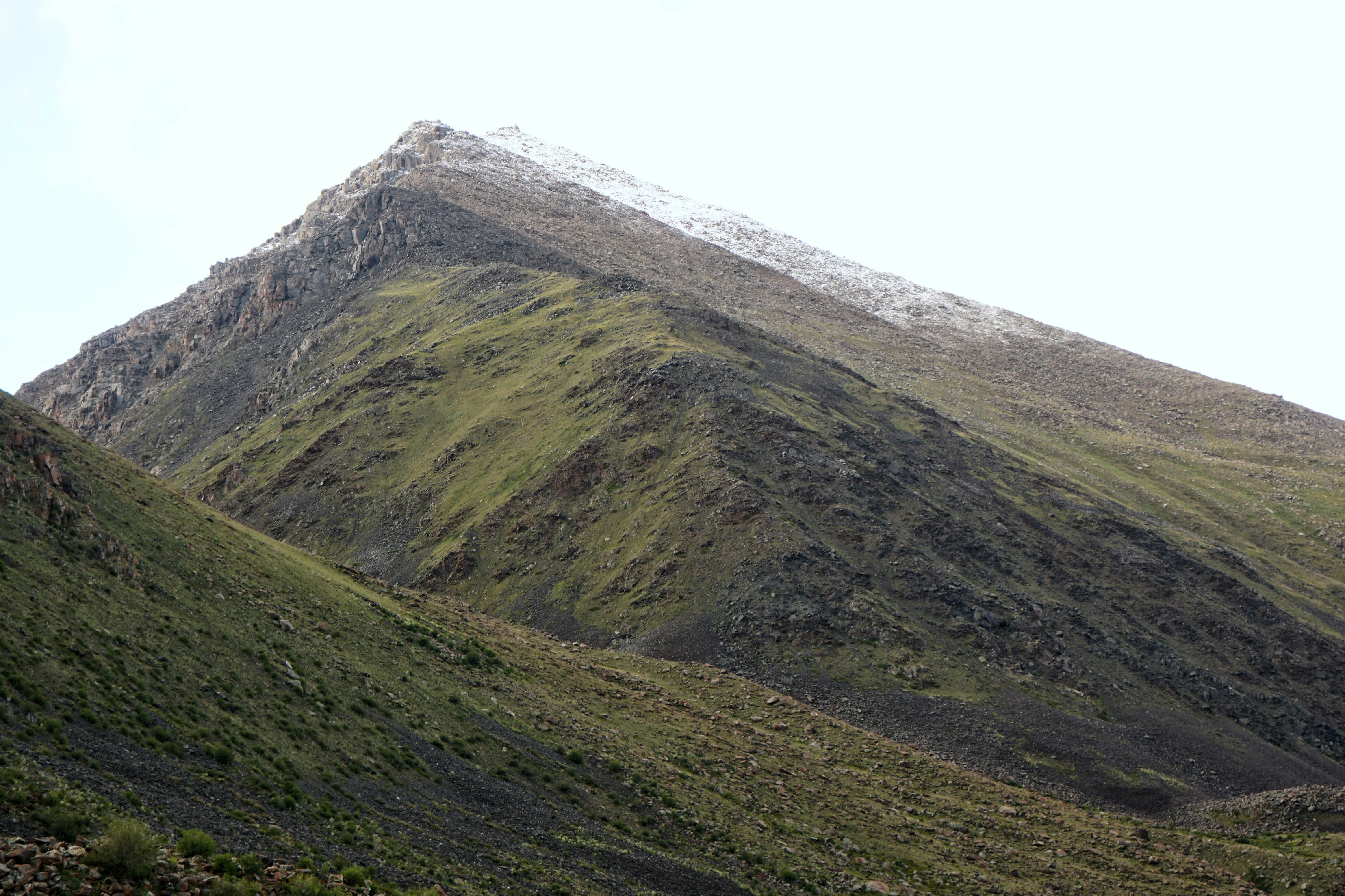 Majestic mountain peak adorned with a dusting of snow, surrounded by lush green slopes and rocky terrain.