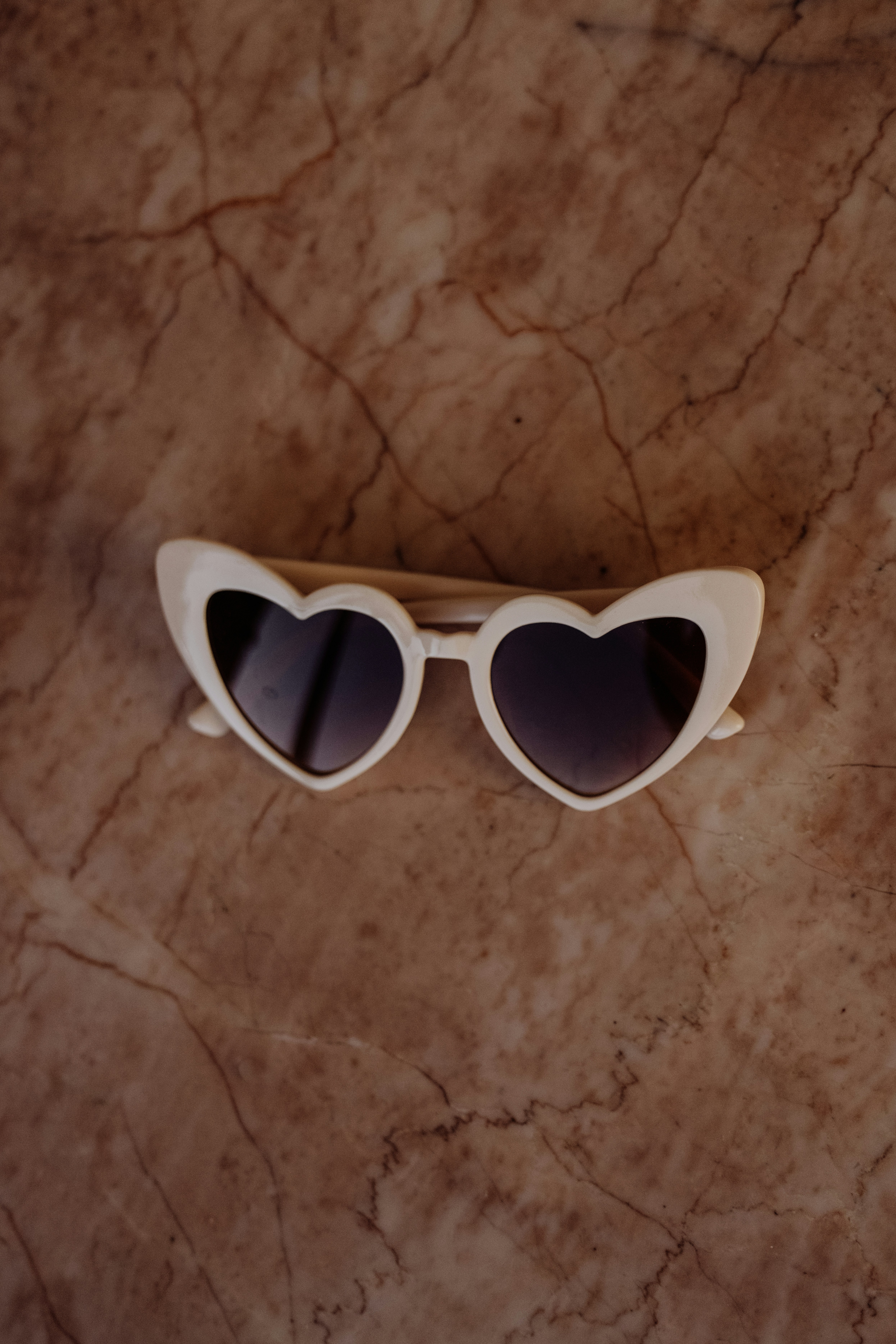 White heart-shaped sunglasses resting on a textured marble surface.