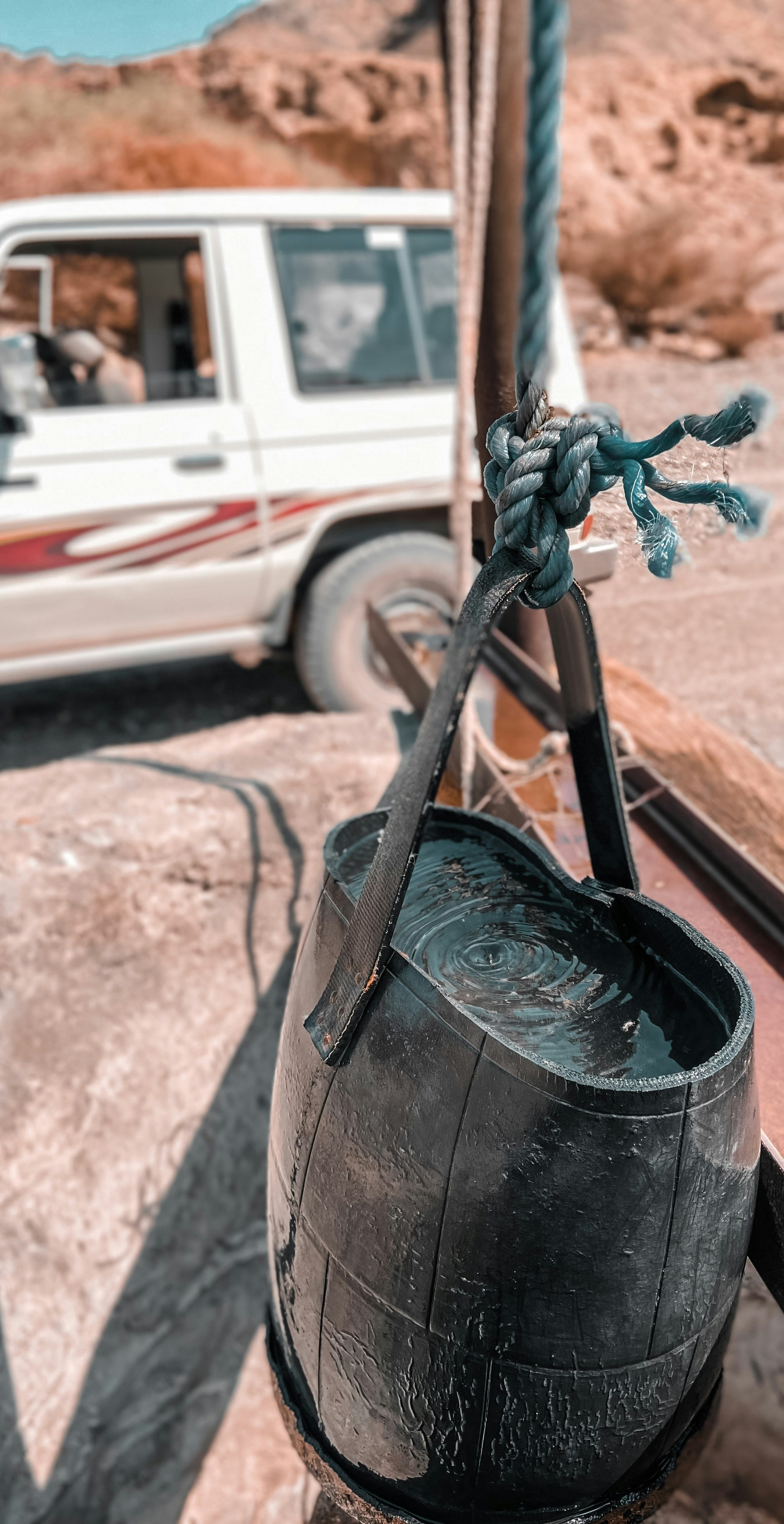 Desert Anchor: A Frayed Rope Secures a Weathered Bucket in Sunlit Terrain