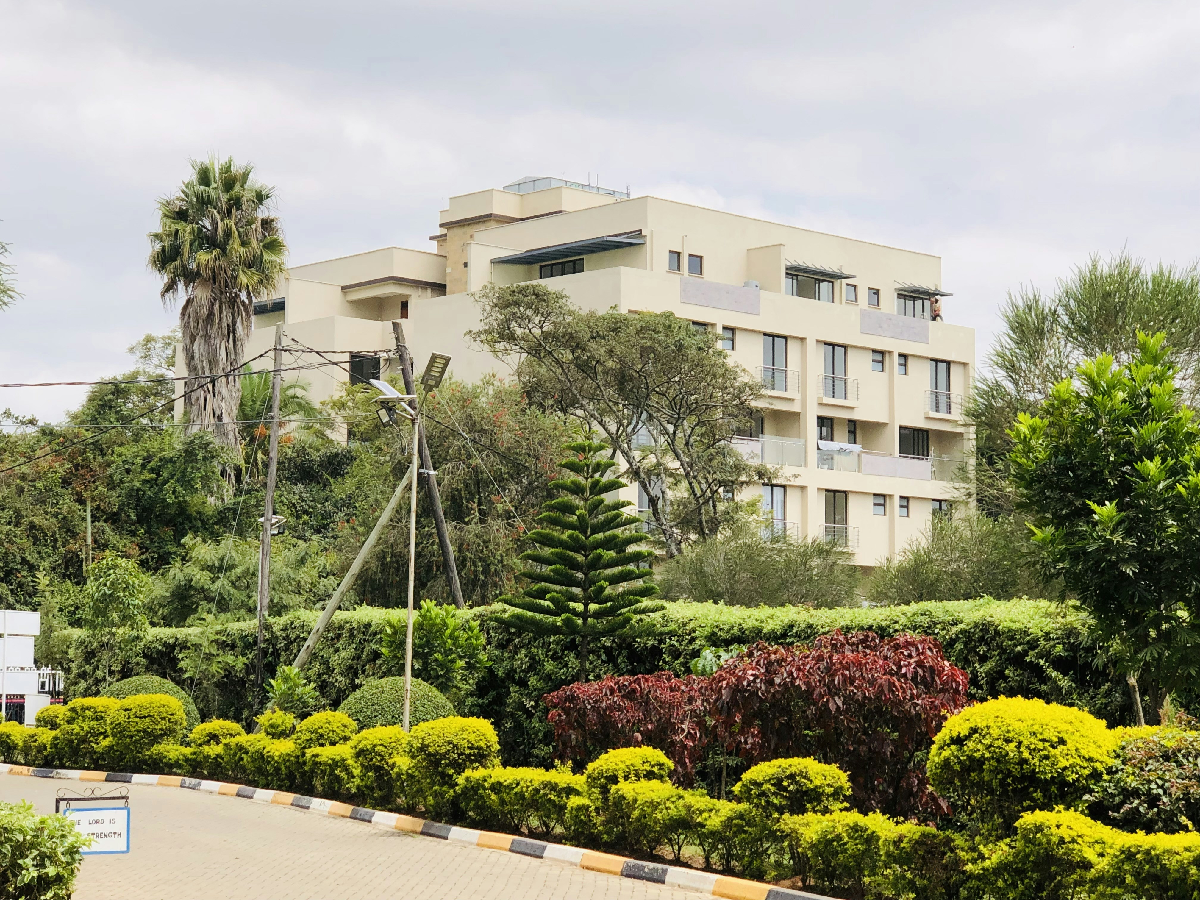 Modern building surrounded by vibrant greenery and landscaped shrubs under a cloudy sky.