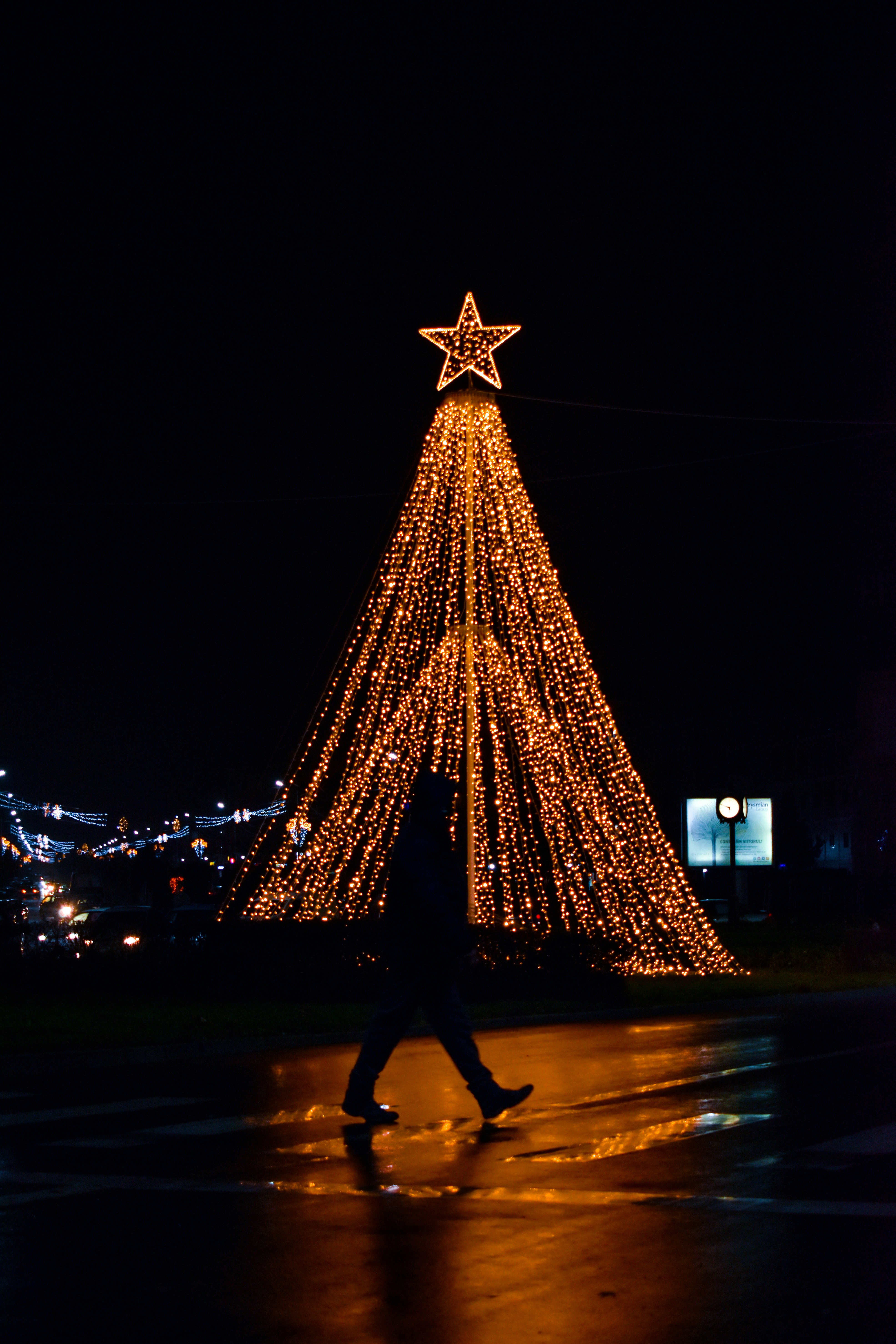 Silhouette of a person walking past a towering, illuminated tree-shaped light display at night.