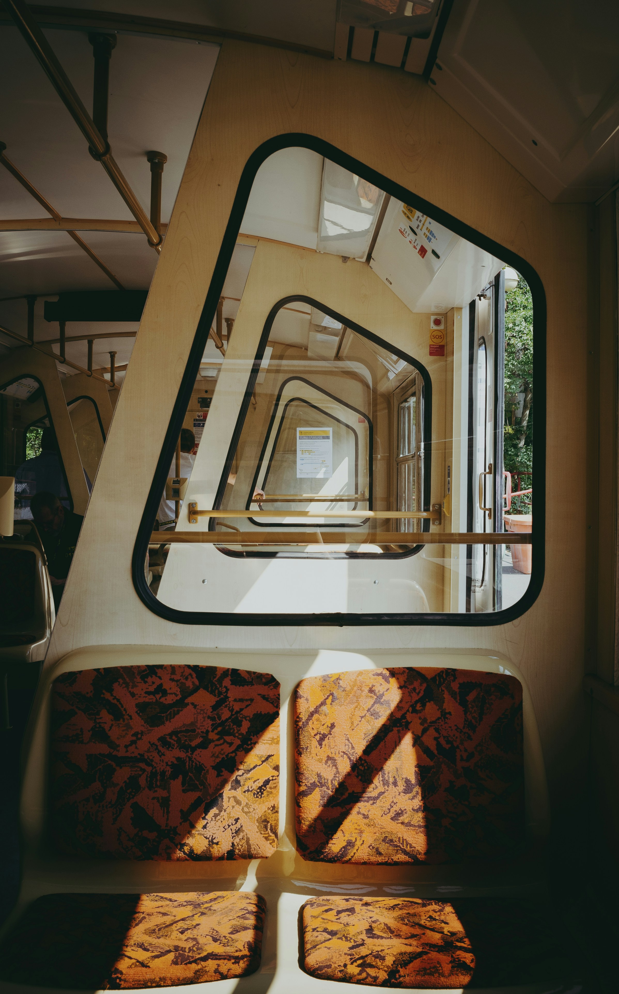 Interior view of a subway train featuring unique angled mirrors and patterned seating. Natural light streams in, creating a warm atmosphere.