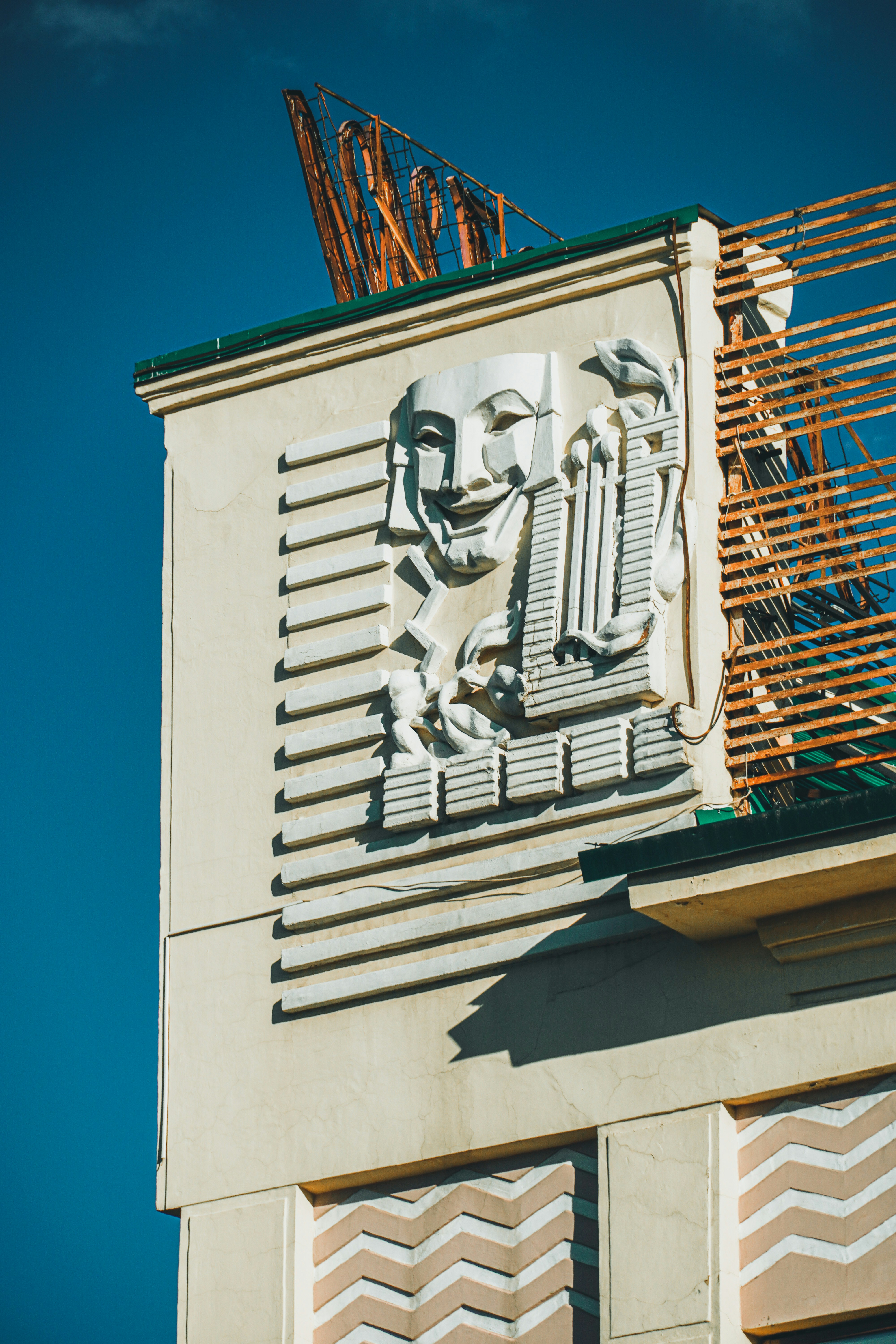 Art Deco-inspired relief sculpture on a building facade, showcasing intricate designs and playful elements against a clear blue sky.