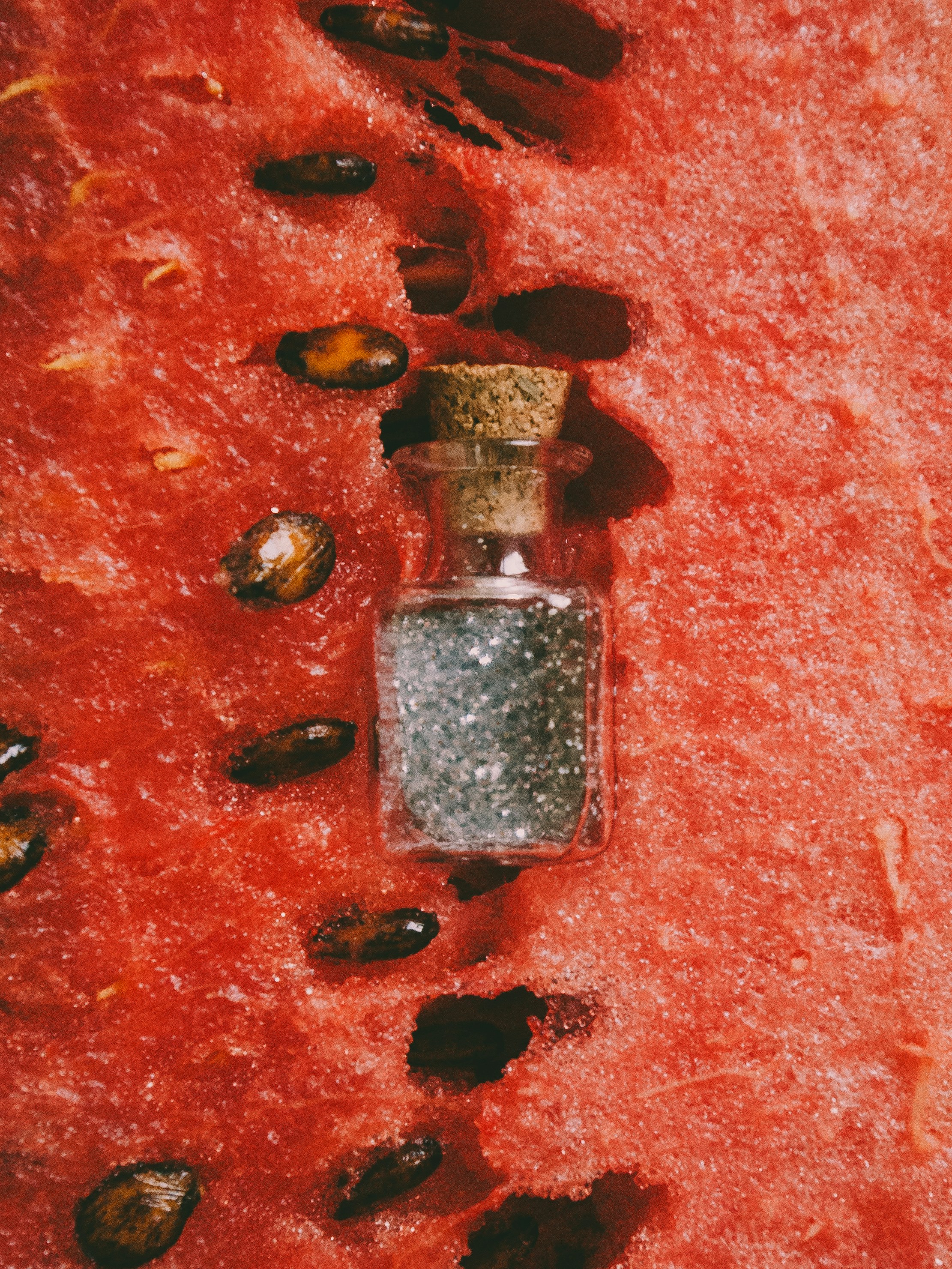 Crimson Macro: A Tiny Corked Vial Resting on a Seed-Stippled Surface