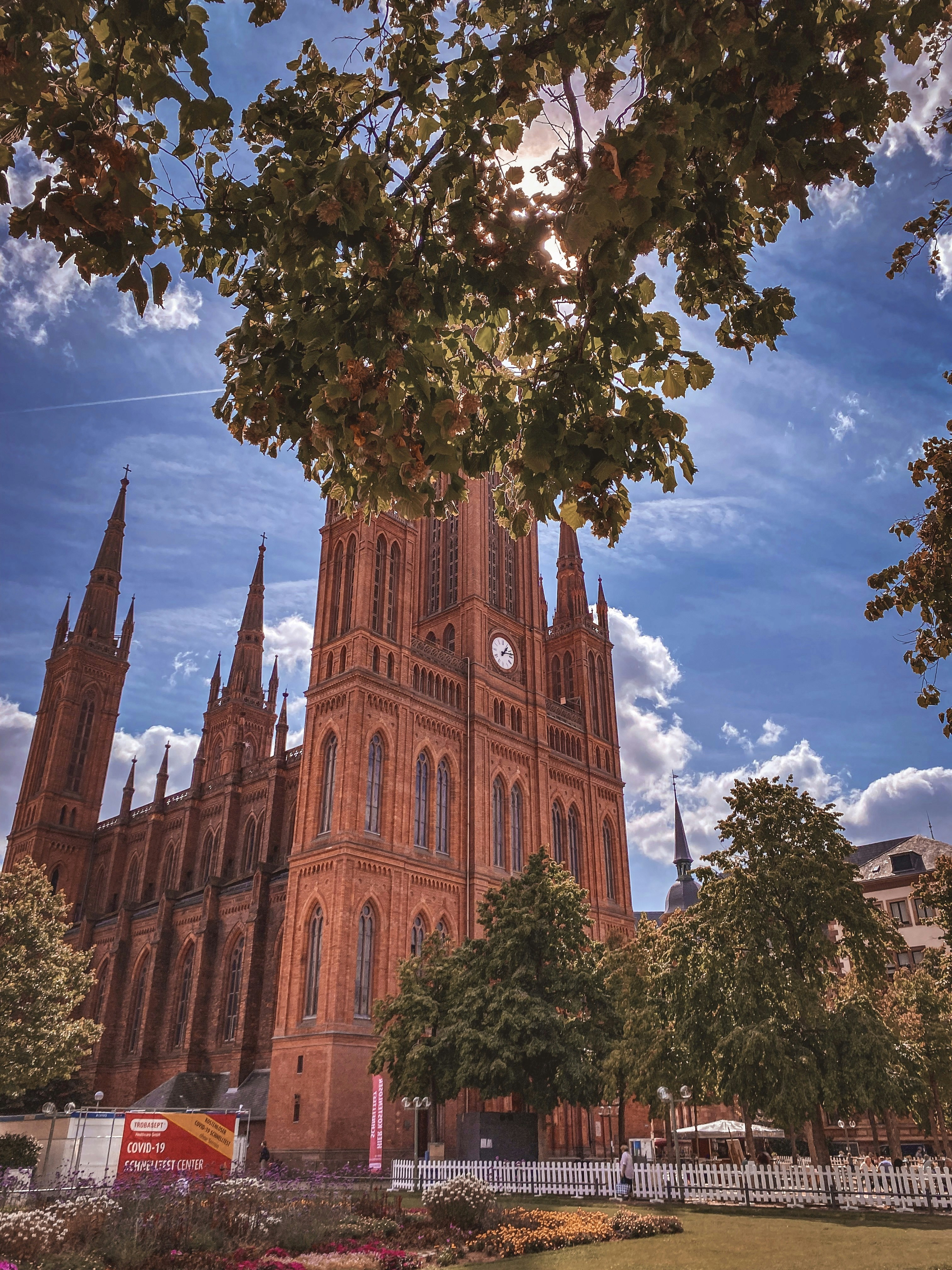 Historic Gothic church framed by lush greenery and a vibrant blue sky with scattered clouds.