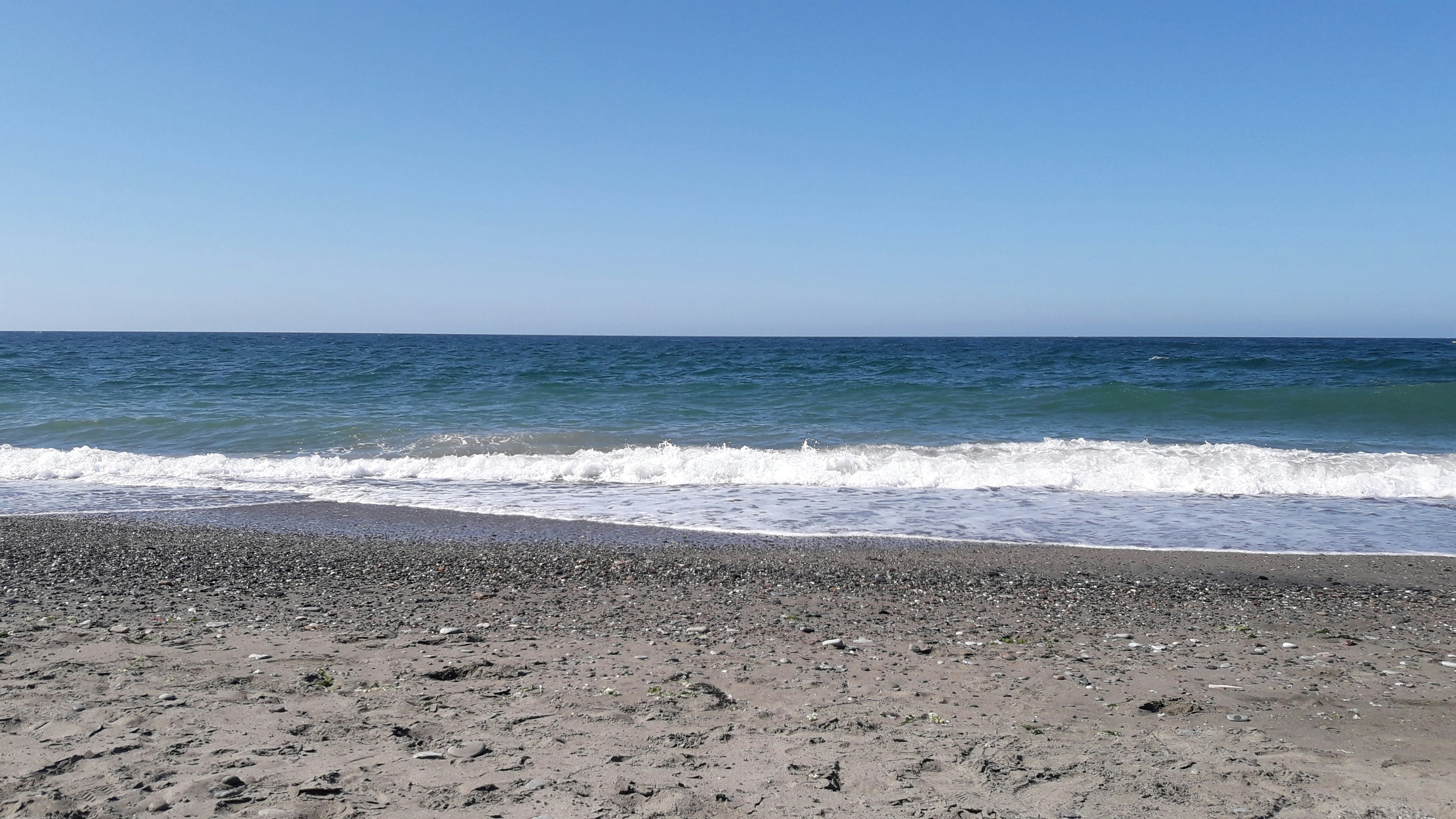 Gentle waves lapping against a sandy beach under a clear blue sky.