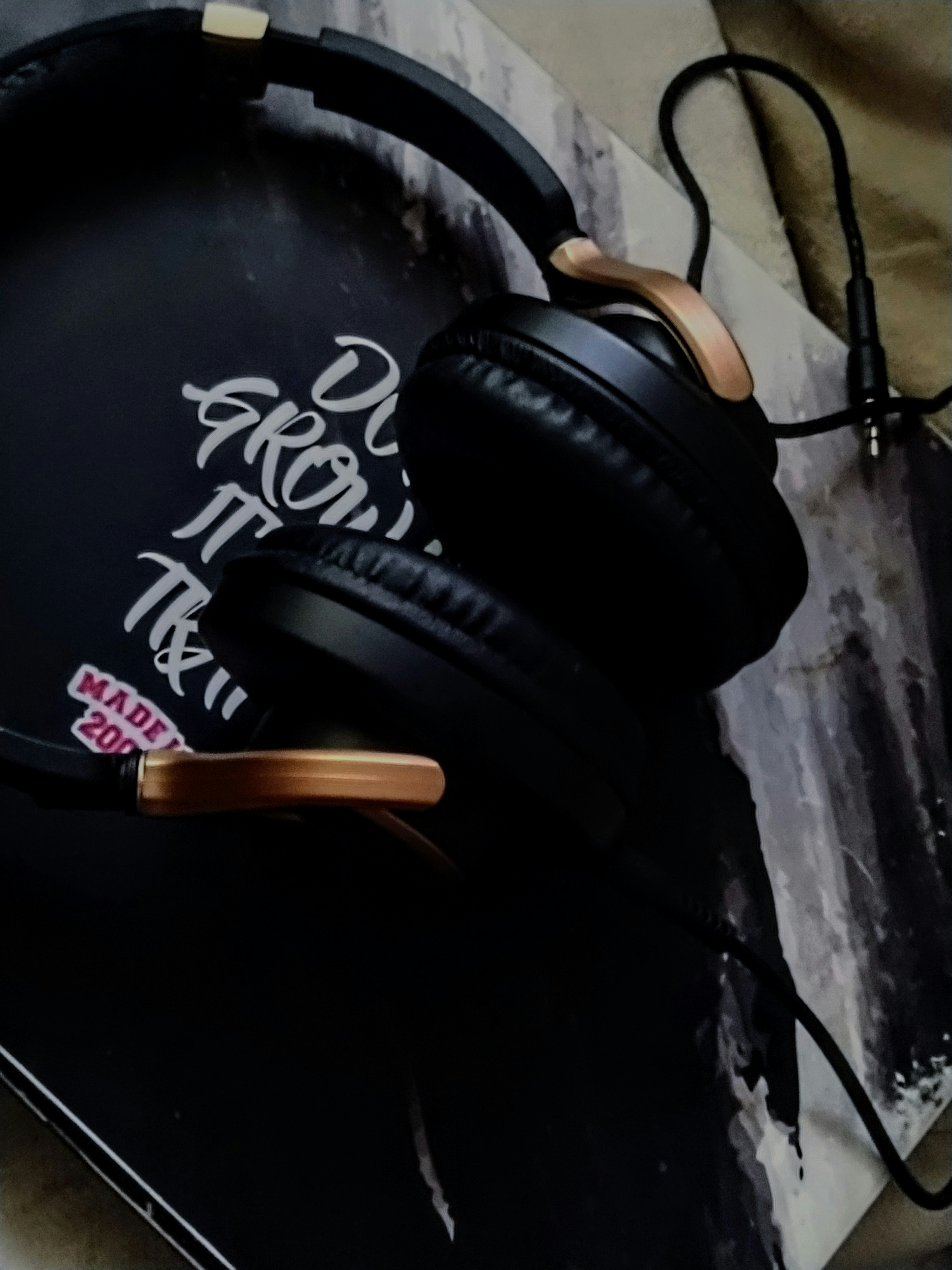 Stylish black headphones with gold accents resting on a textured notebook with artistic lettering. Perfect for music lovers and creatives.