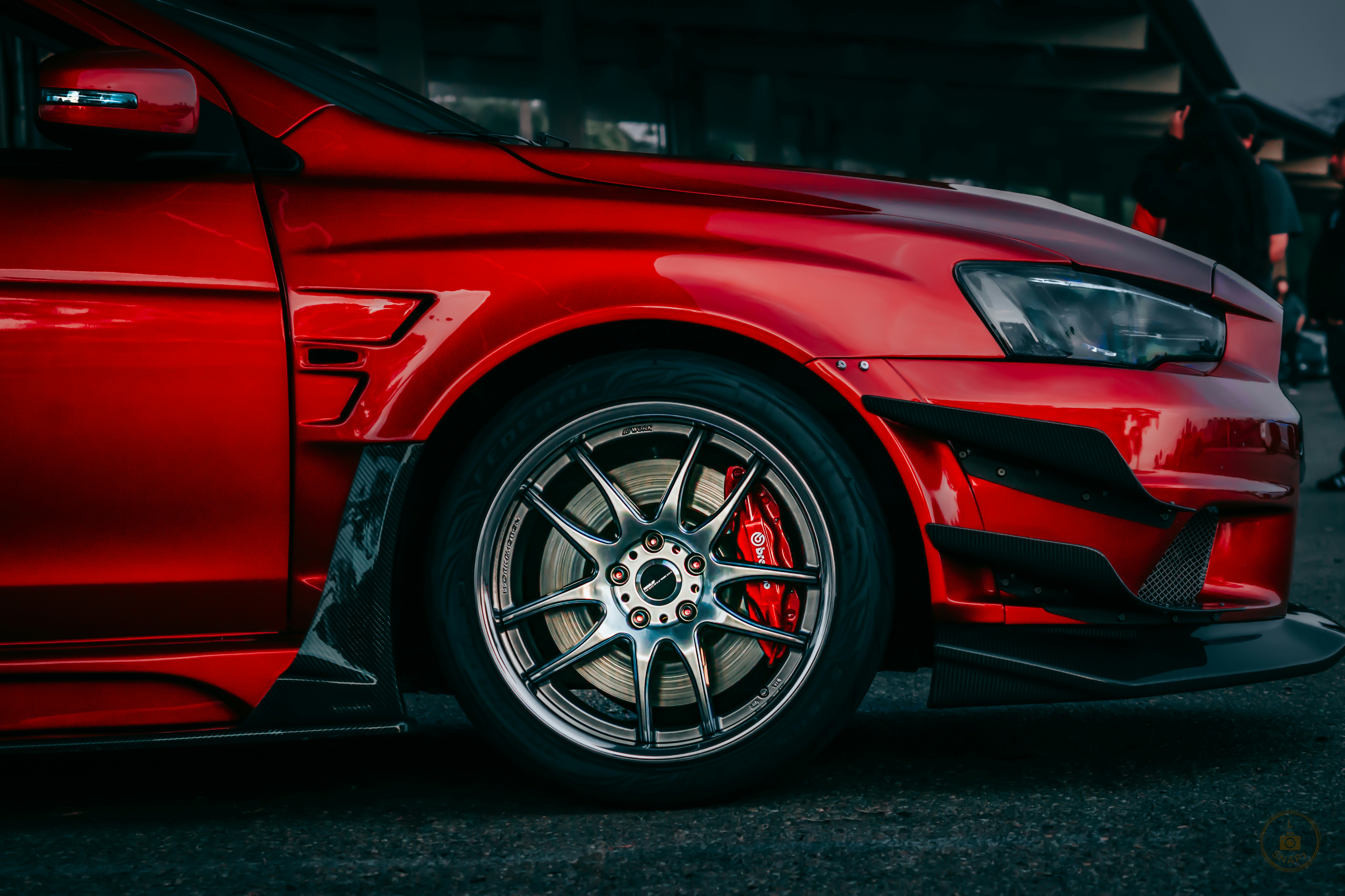 Close-up of a modified red sports car showcasing its intricate wheel design and sleek body lines.