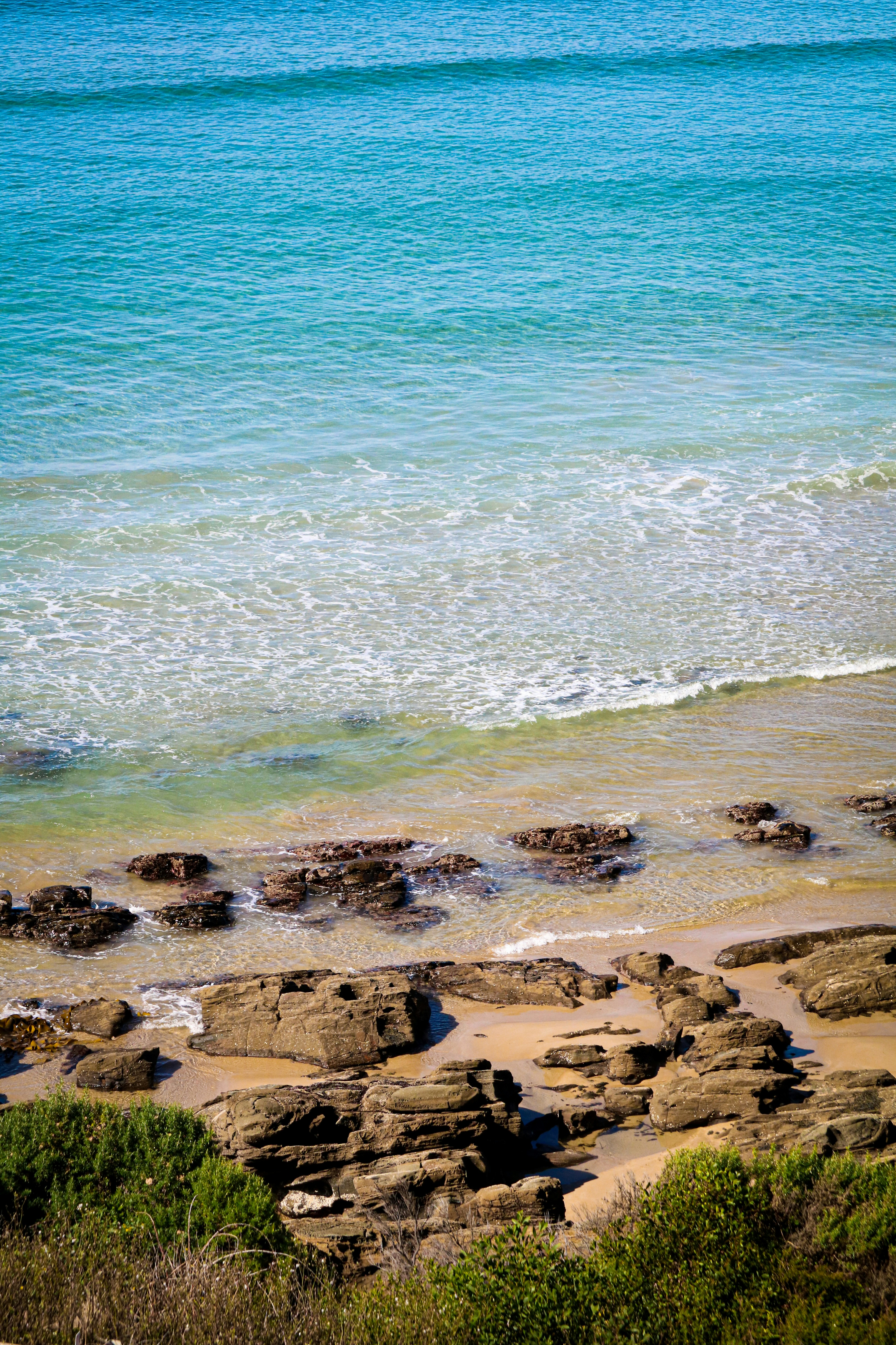 Gentle waves caressing rocky shorelines under a clear blue sky, showcasing the interplay of land and sea.