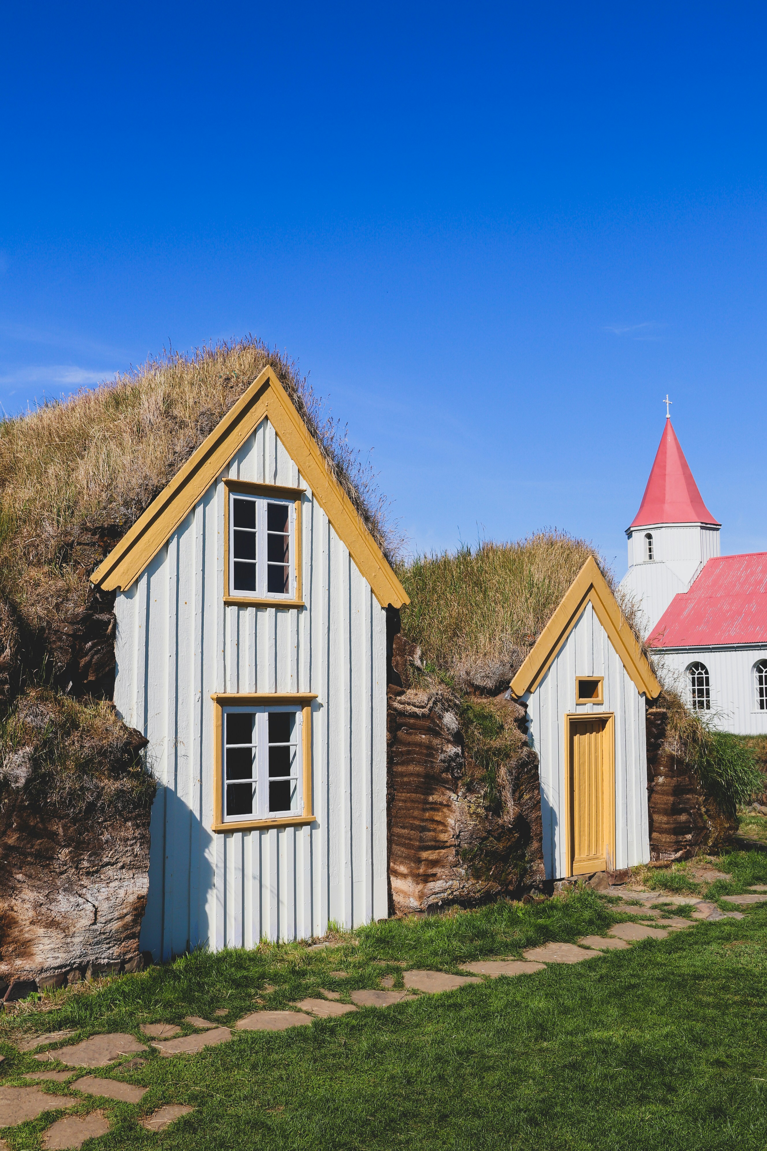 Turf-roofed cottages along a sunlit path beneath a cerulean sky