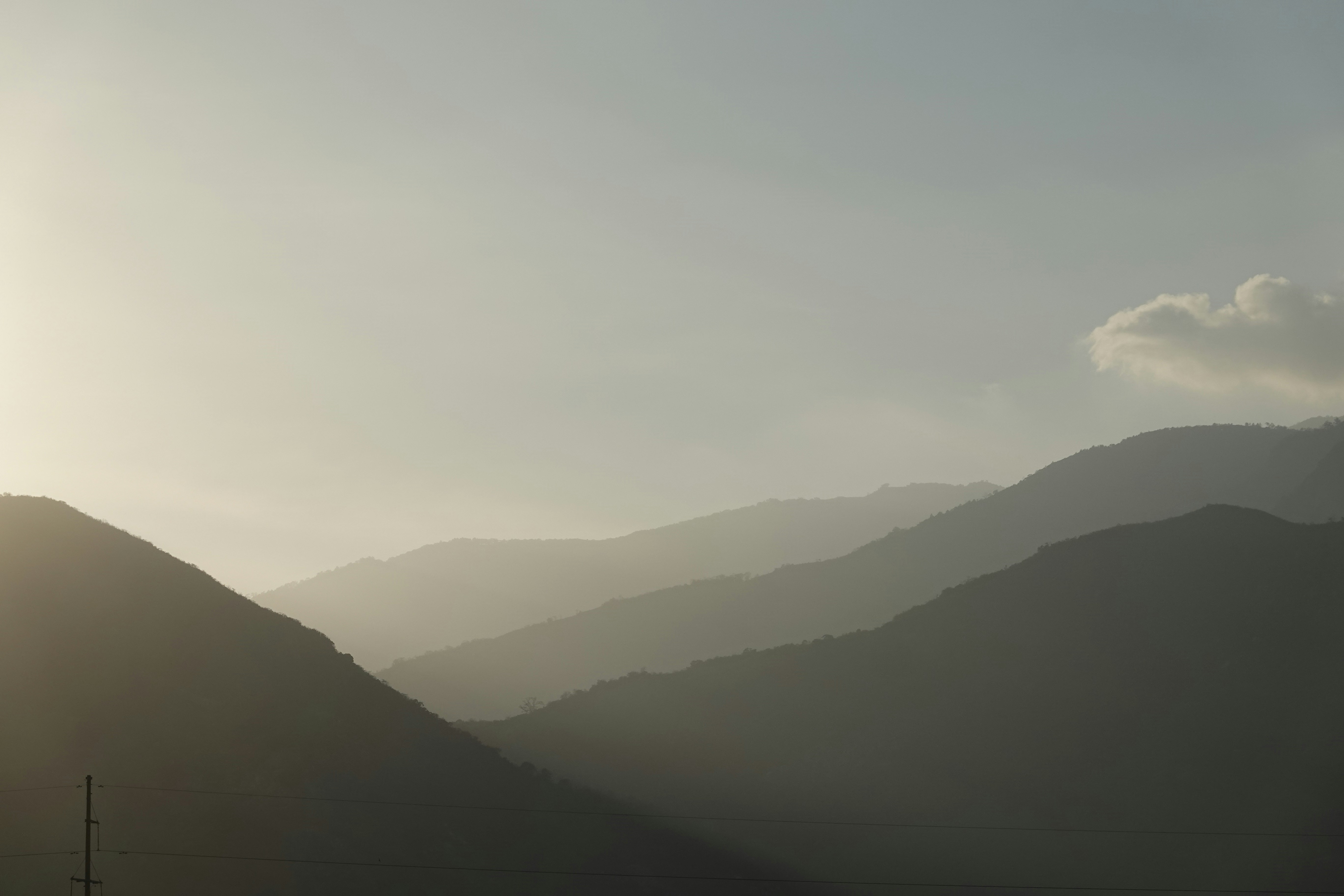 Softly layered mountains fade into the horizon under a gentle sunset glow, creating a serene atmosphere.