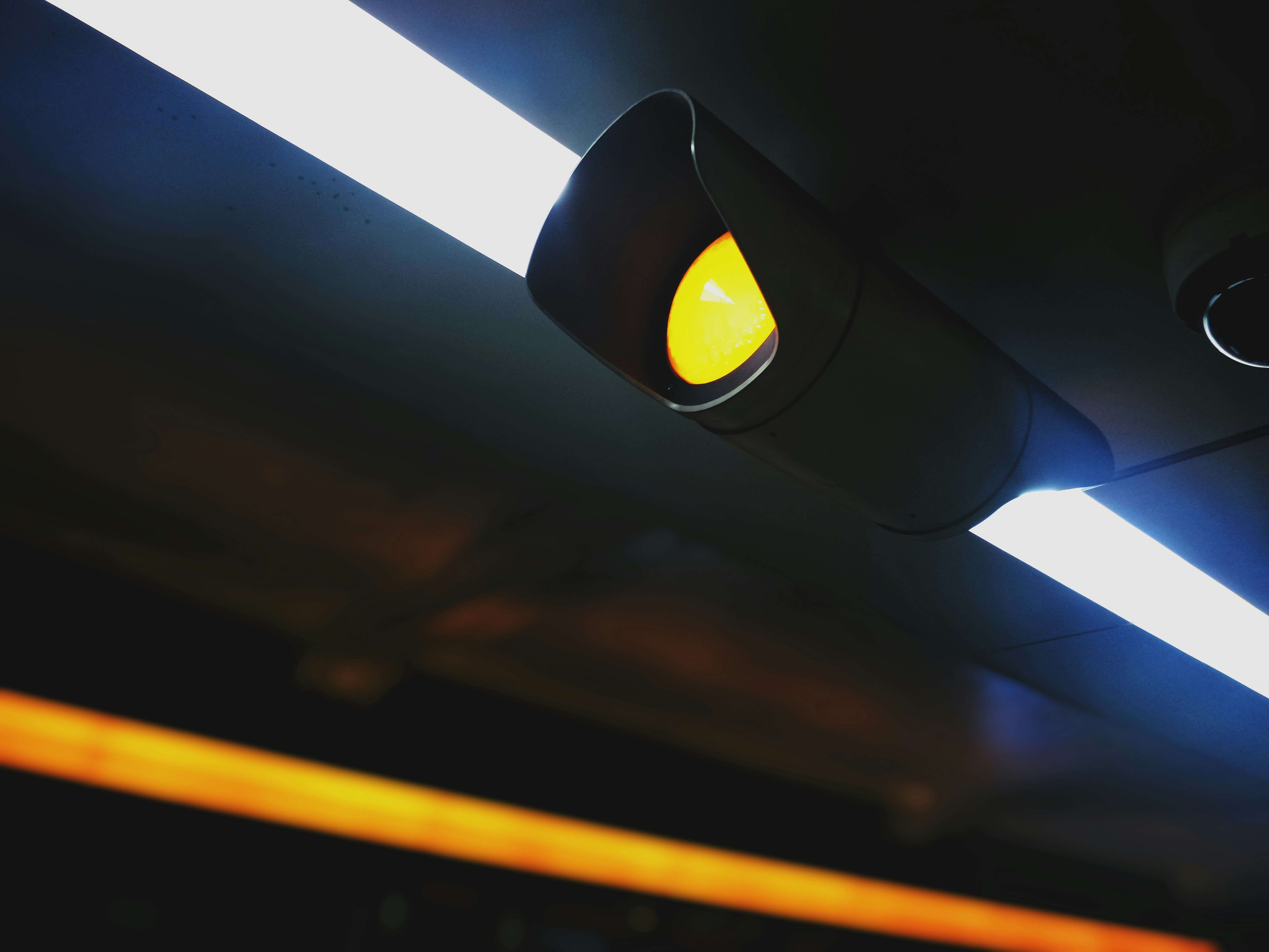 Yellow signal light suspended from ceiling with contrasting linear lighting in a dark setting.