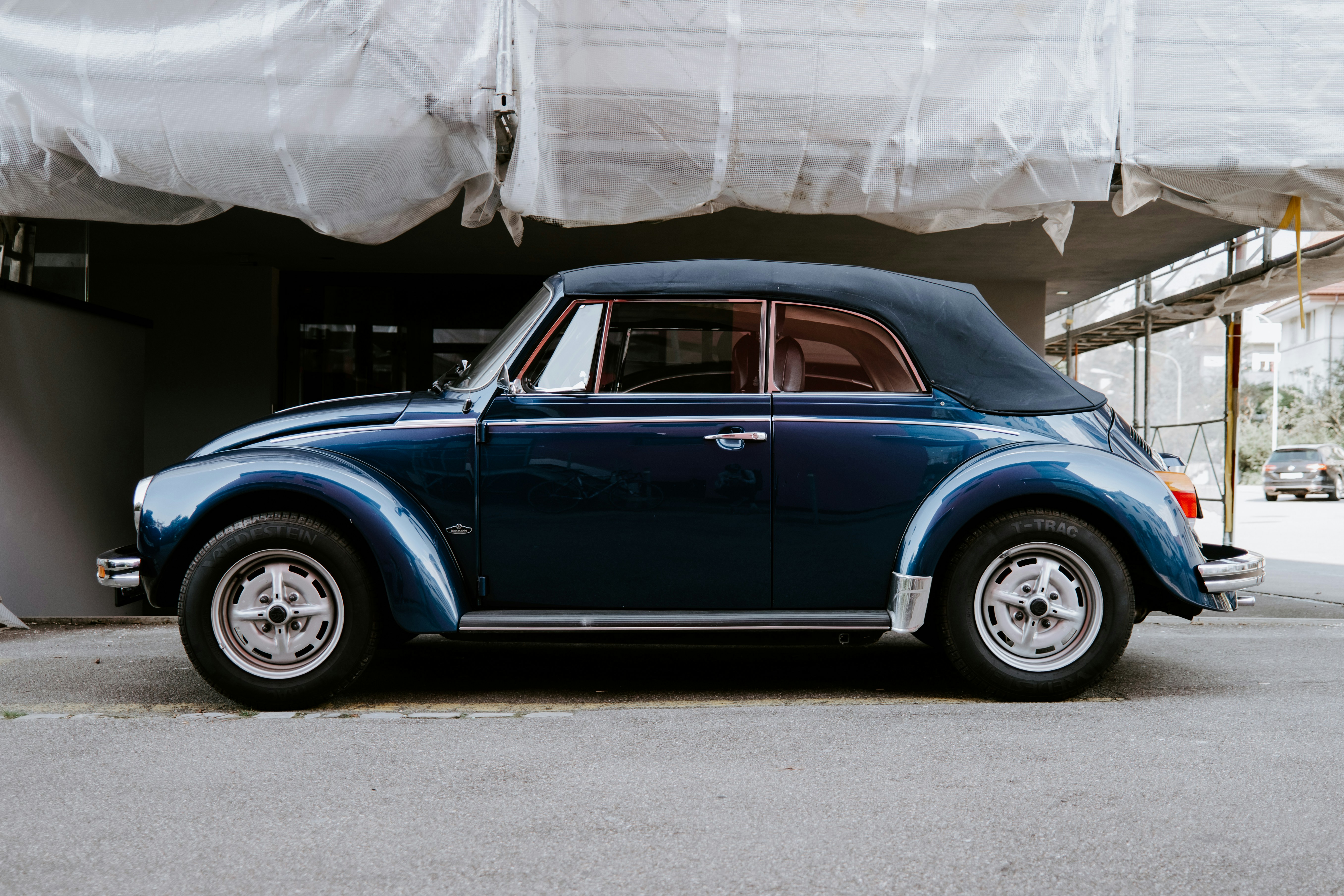 A vintage convertible car parked beneath a covered structure, showcasing its sleek lines and rich blue color.