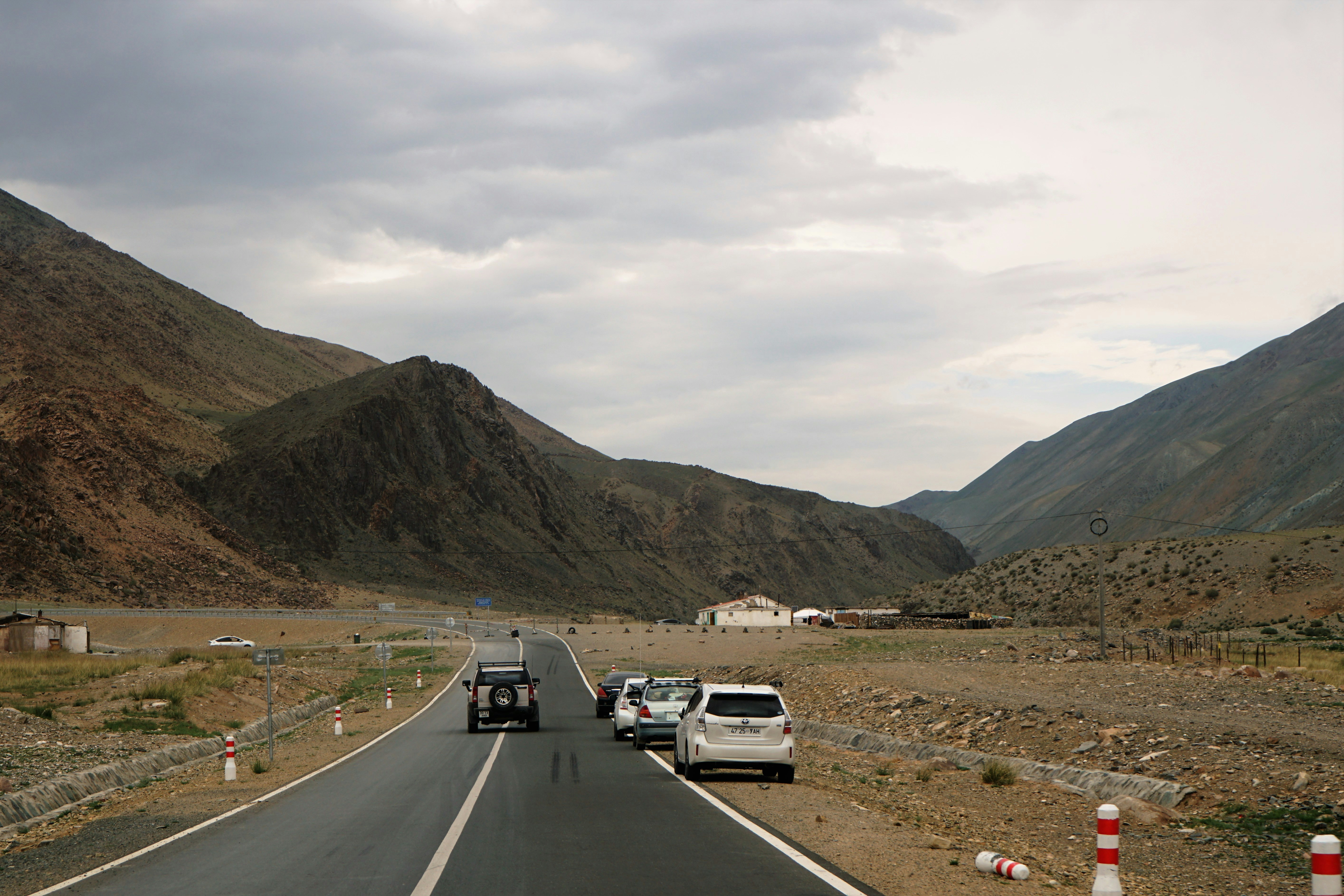 A winding road cuts through a mountainous landscape, flanked by parked vehicles and dramatic slopes. The scene captures the essence of travel in remote areas.
