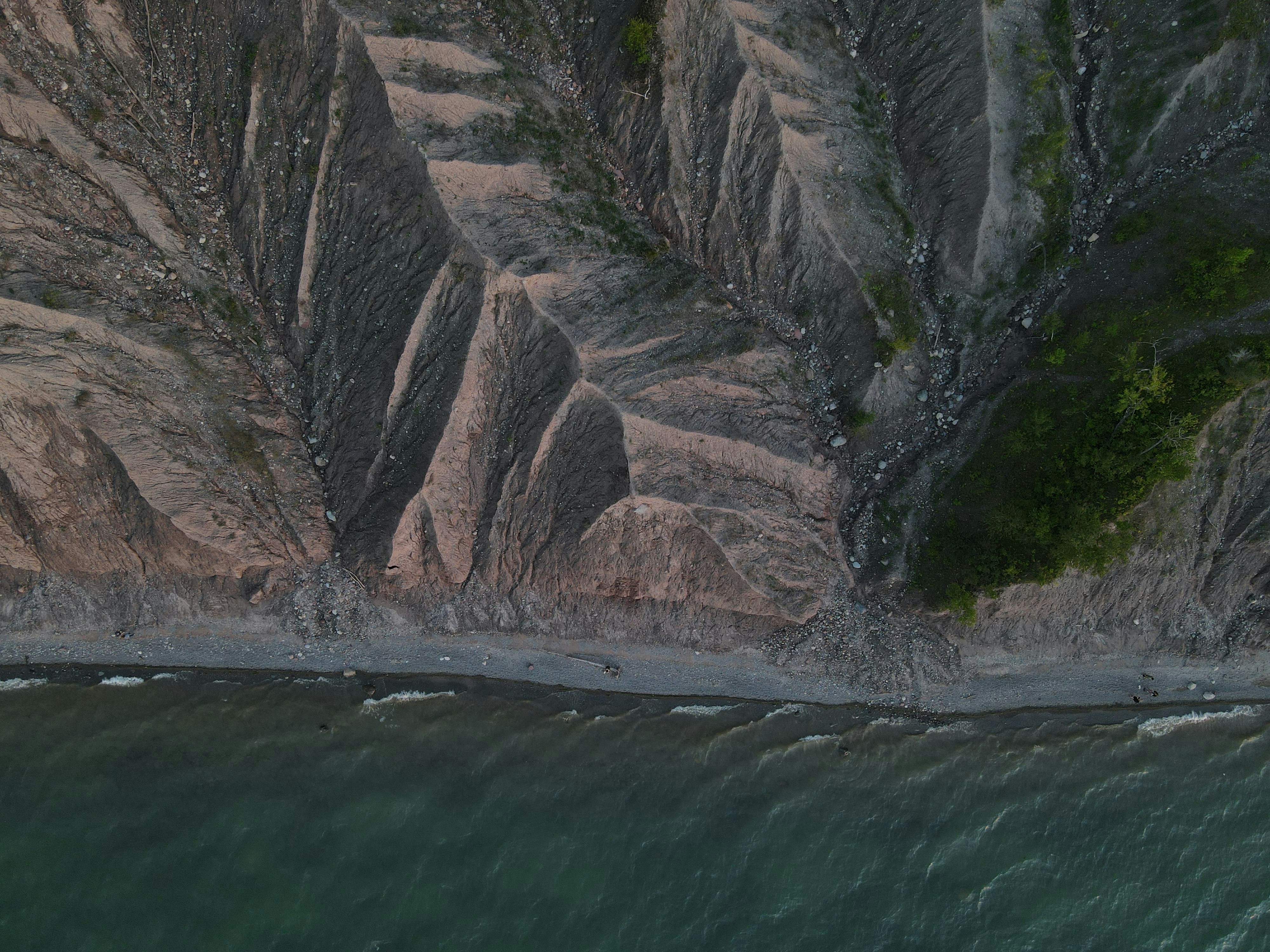 Aerial view of rugged coastal cliffs revealing intricate geological formations and a serene shoreline below.