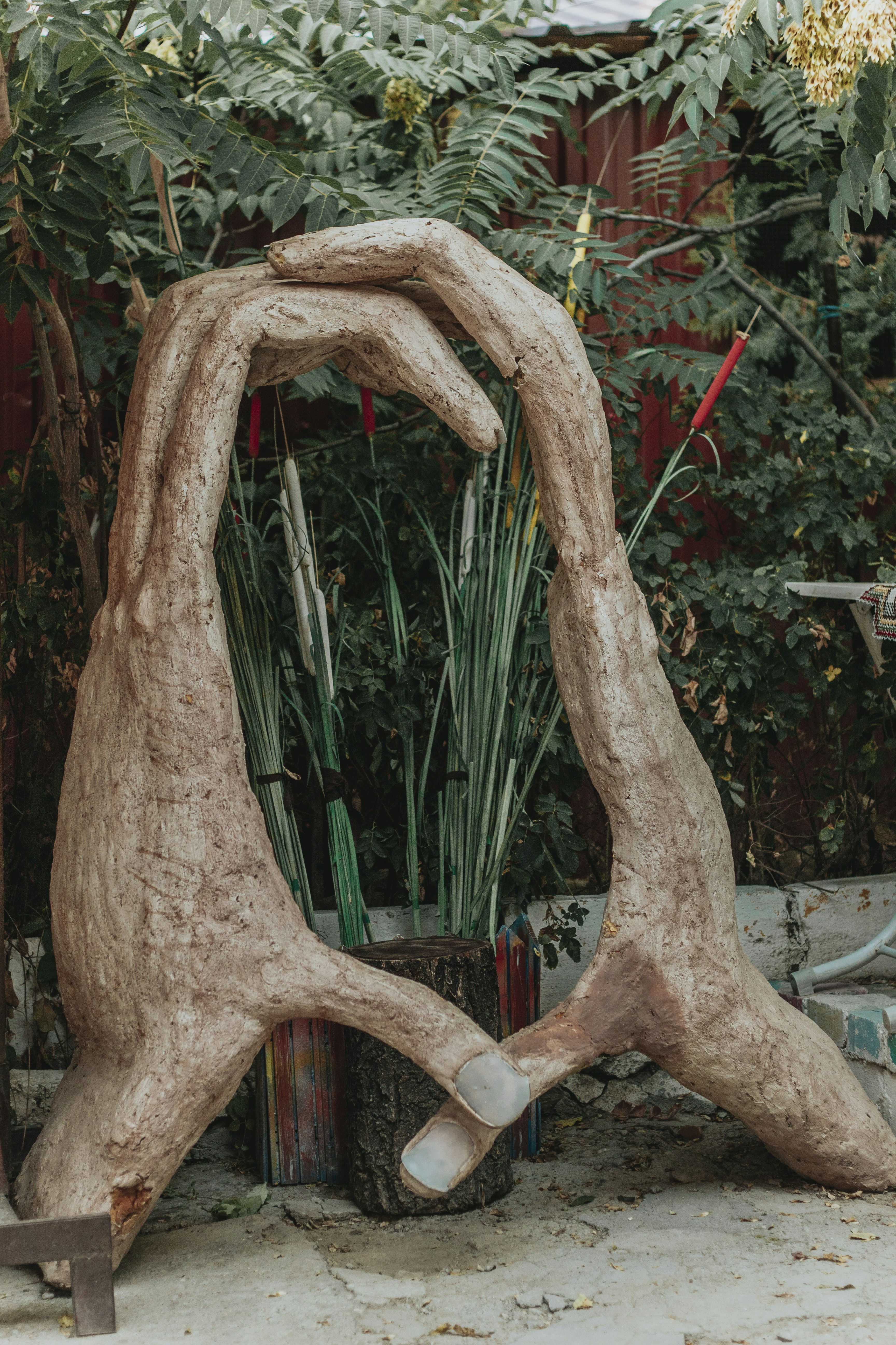 Artistic wooden sculpture of two hands forming a heart shape, surrounded by lush greenery and tall reeds.