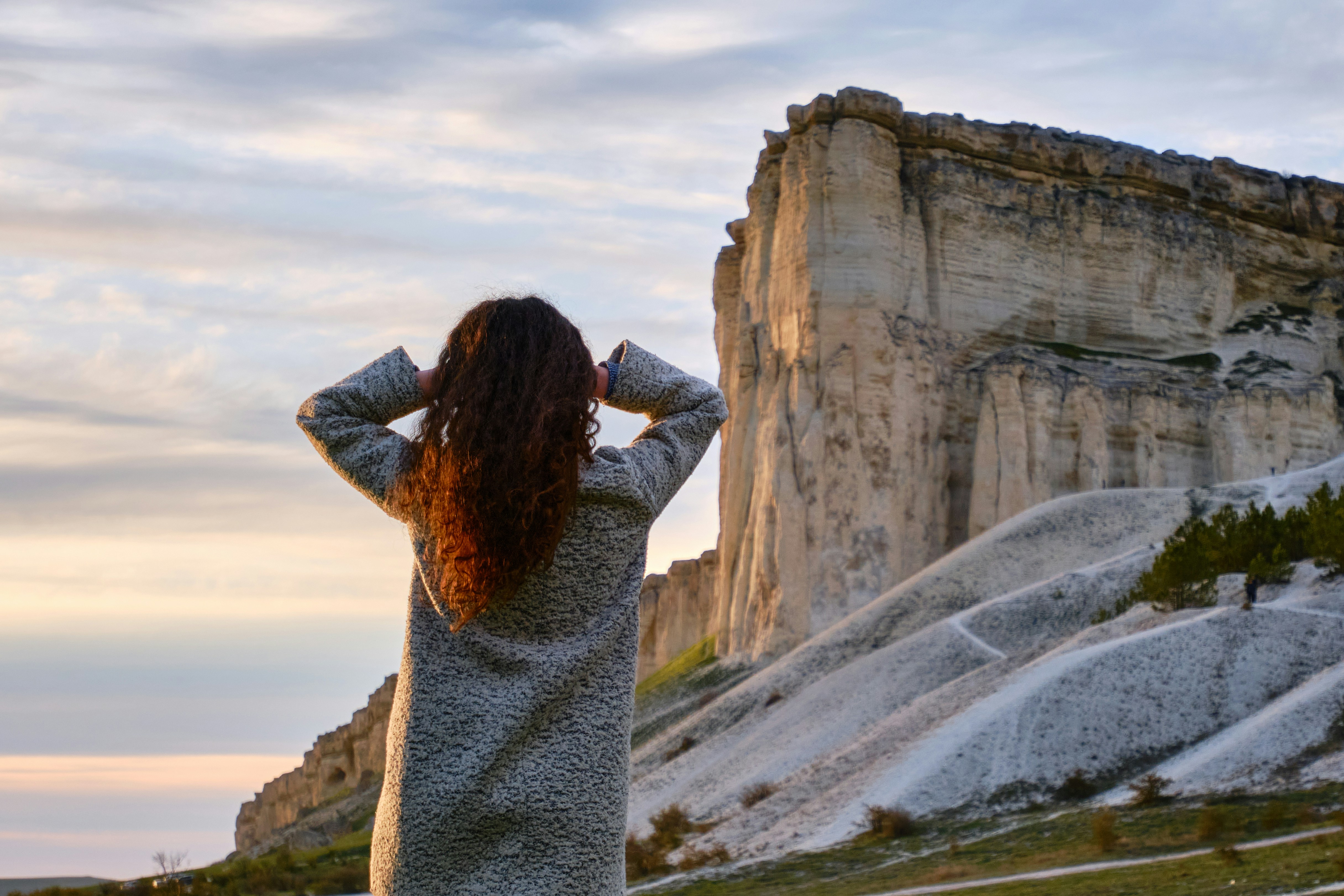 Person in a Cozy Coat Faces a Majestic Cliff as Sunset Proceeds
