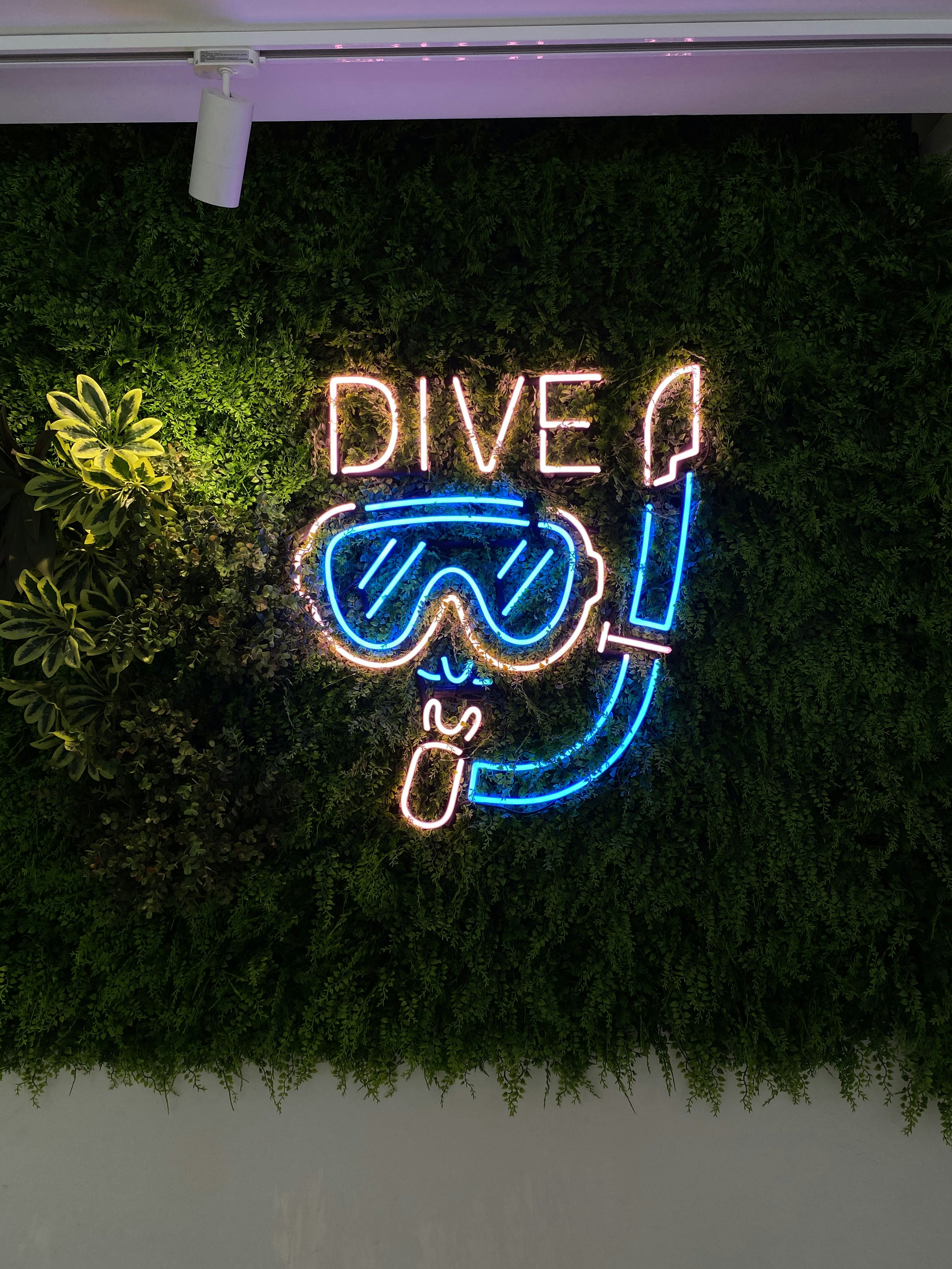 DIVE Neon on a Living Green Wall: The Diving-Goggles Sign Amid Dense Foliage