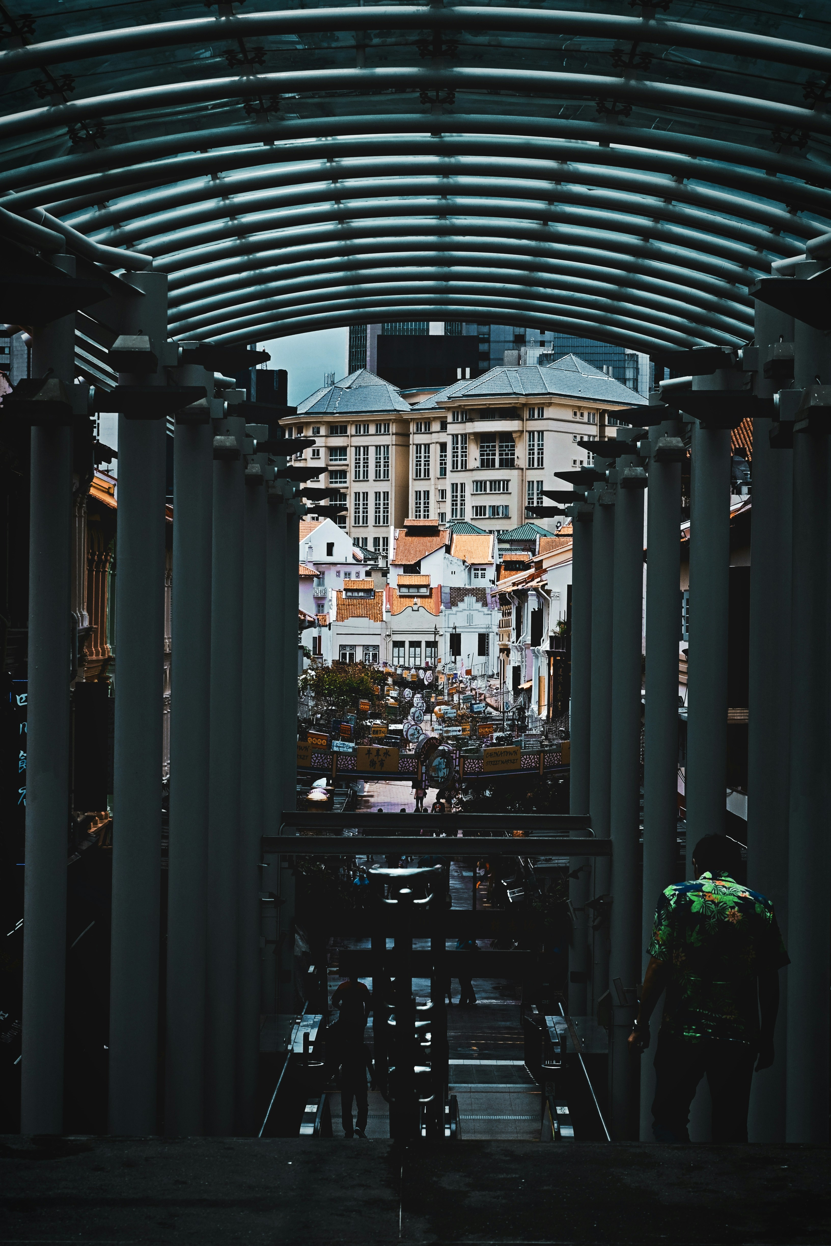 A vibrant urban scene framed by modern arches, showcasing the blend of historical and contemporary architecture in a bustling city. The foreground features pedestrians amidst a lively marketplace.