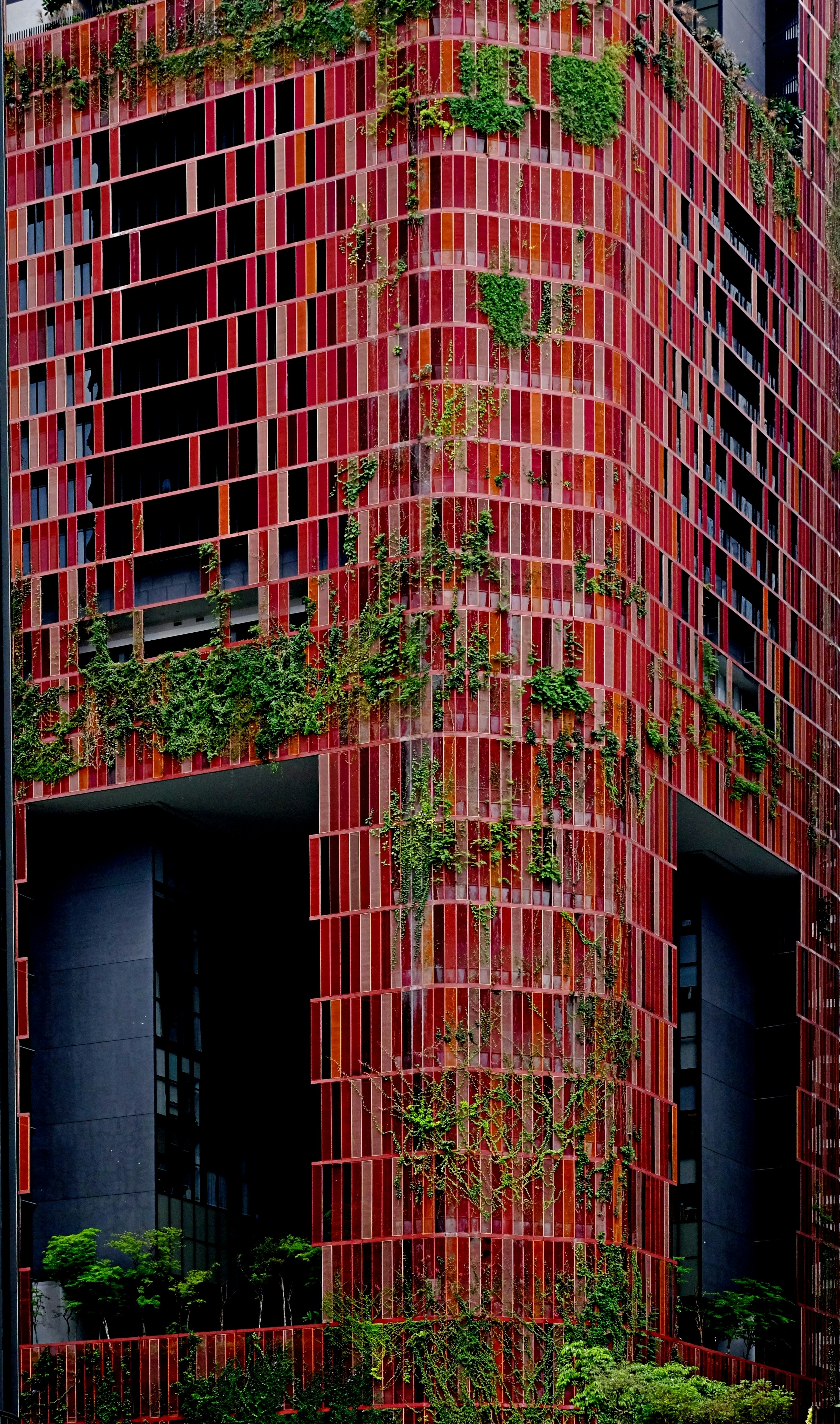 Vibrant building facade adorned with red panels and lush greenery, showcasing a harmonious blend of nature and urban design.