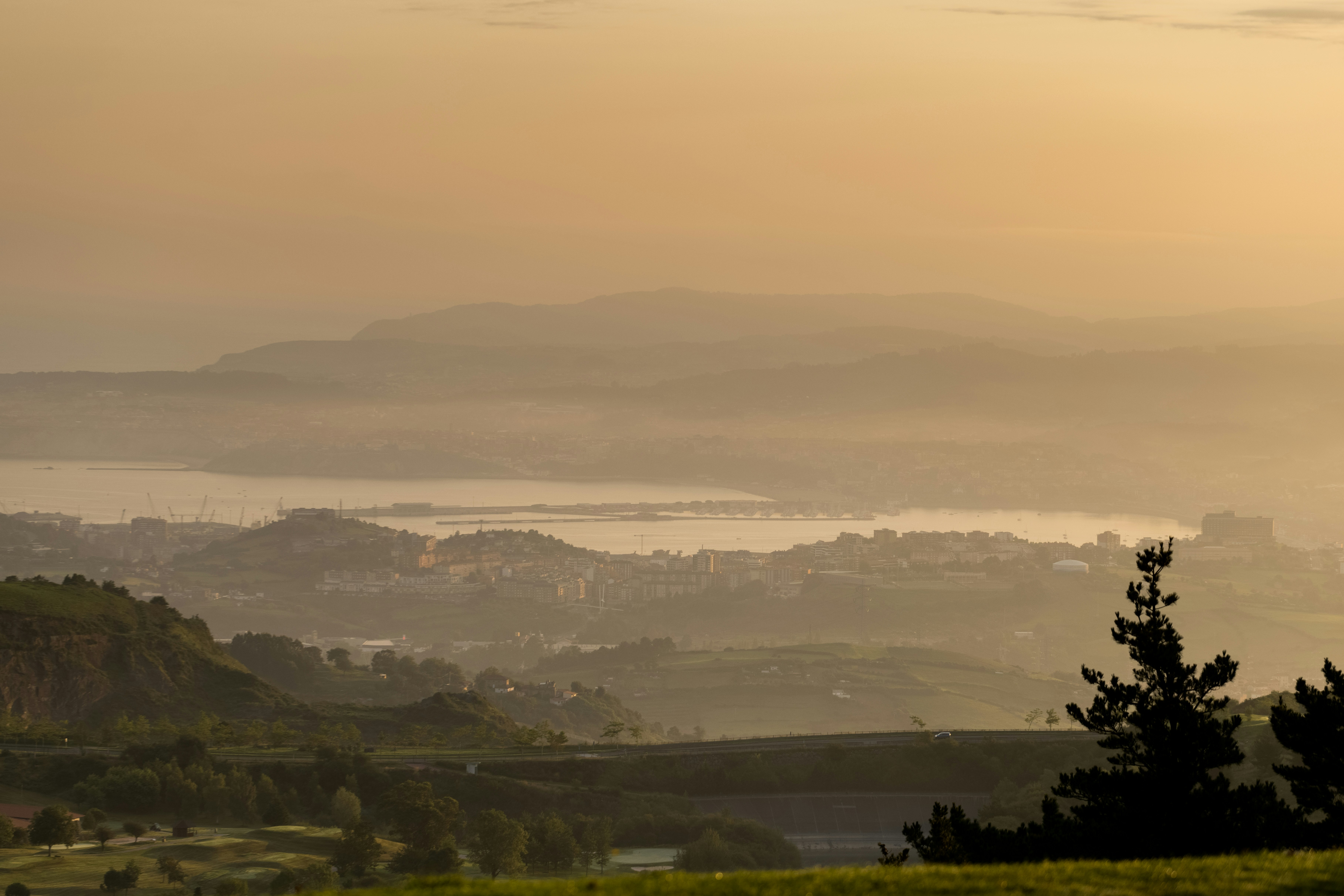 Misty hills under a golden sunrise with a serene sea in the distance.