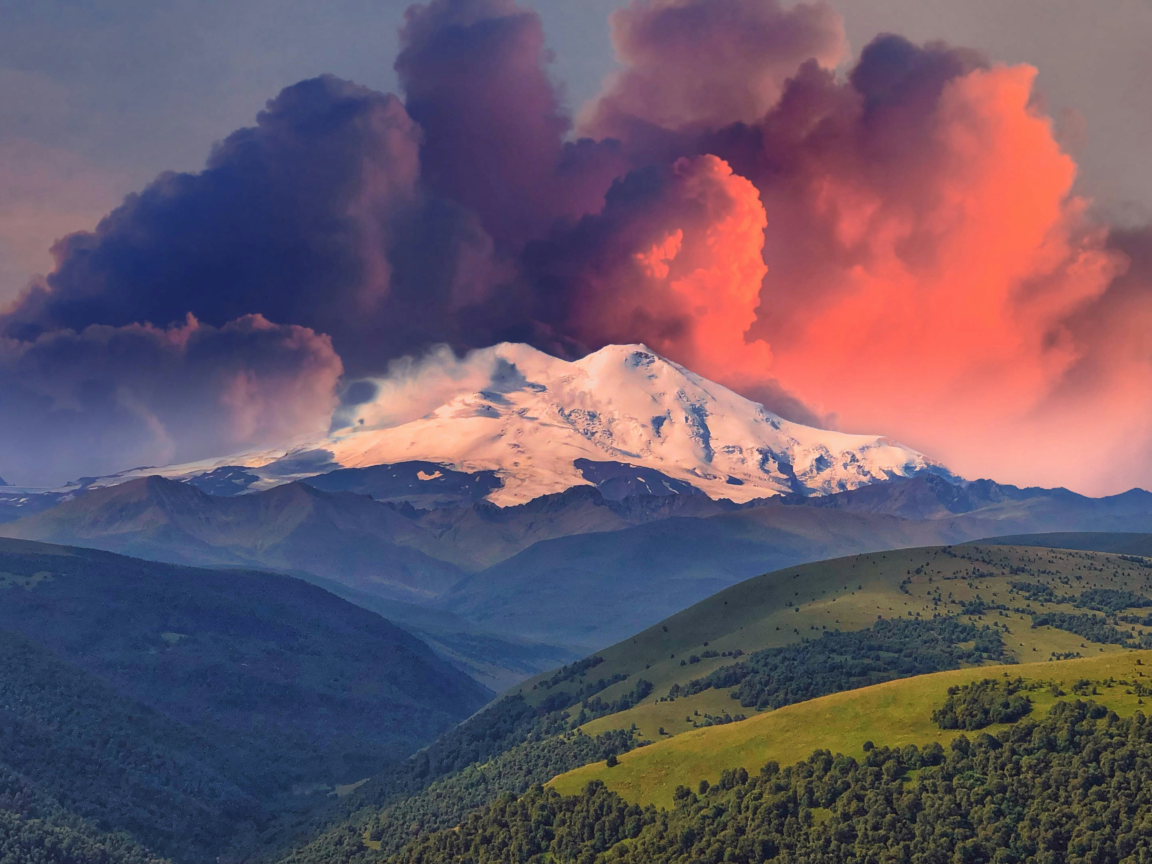Majestic snow-capped peak enveloped by vibrant, swirling clouds at sunset, showcasing nature's dramatic palette.