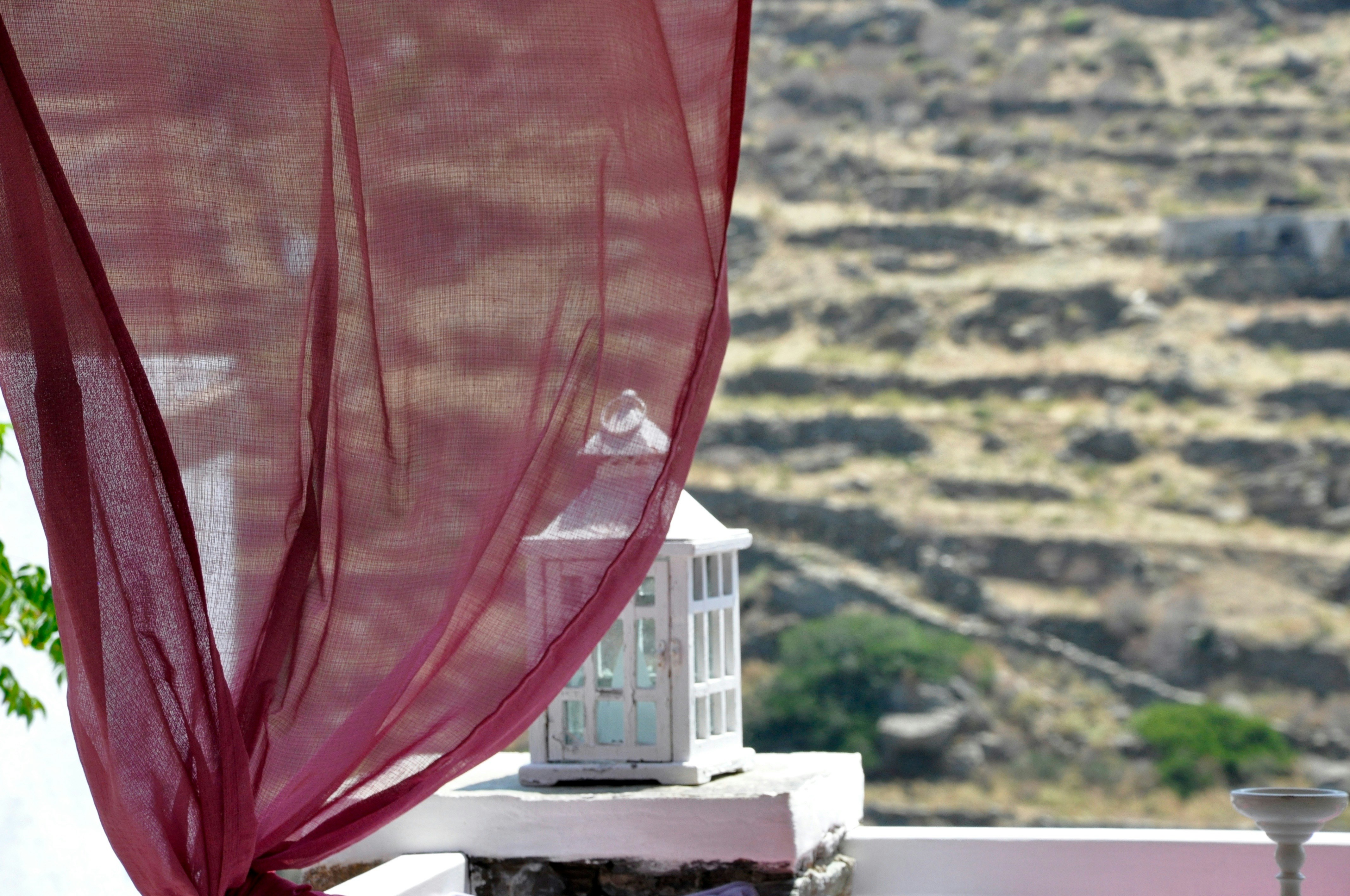 Lantern on a sunlit terrace framed by burgundy curtain