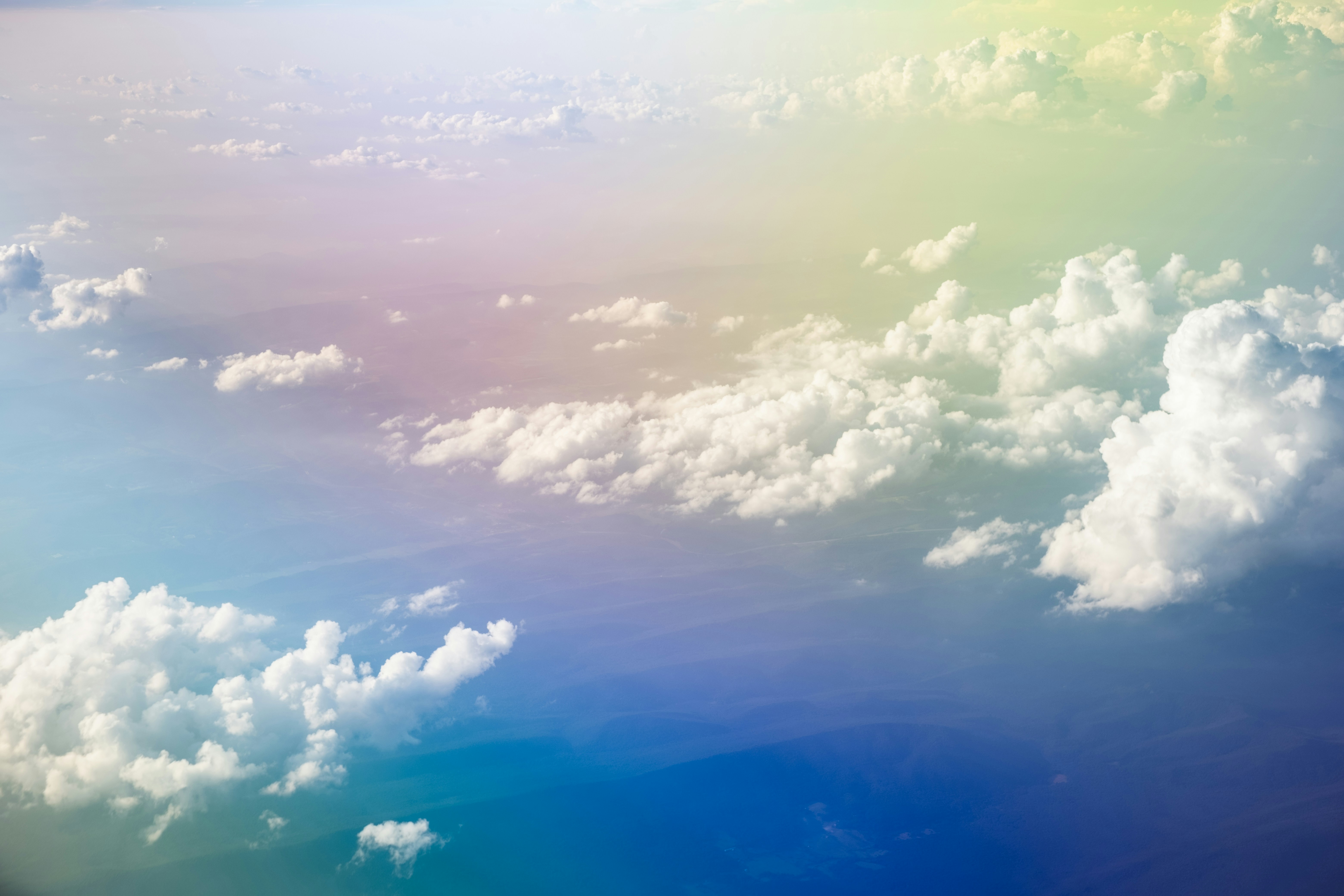 A vibrant aerial view showcasing a gradient of colors blending seamlessly with fluffy clouds against a vast sky. 