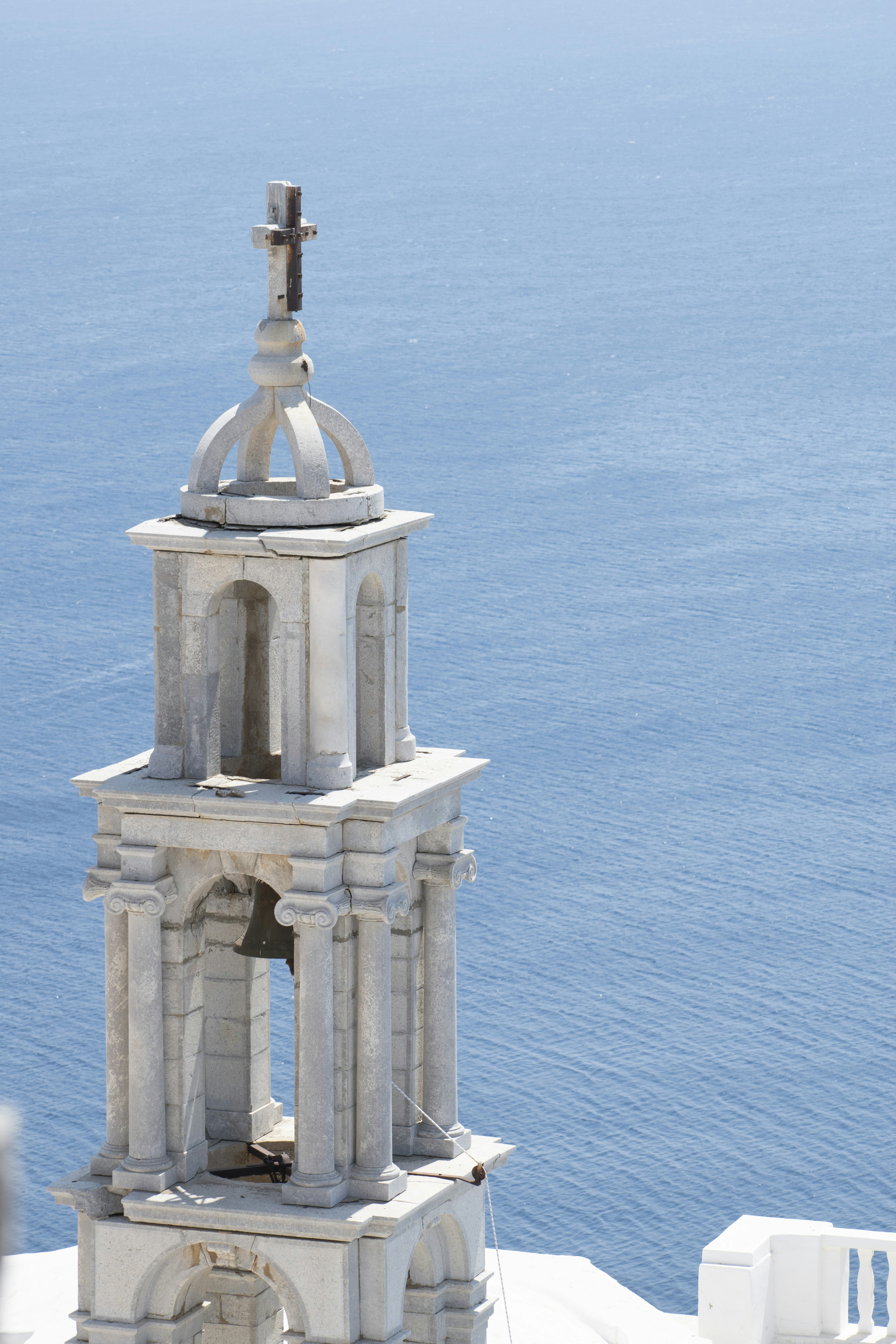 Bell tower with a cross overlooking the serene Aegean Sea, showcasing architectural elegance against a tranquil backdrop.
