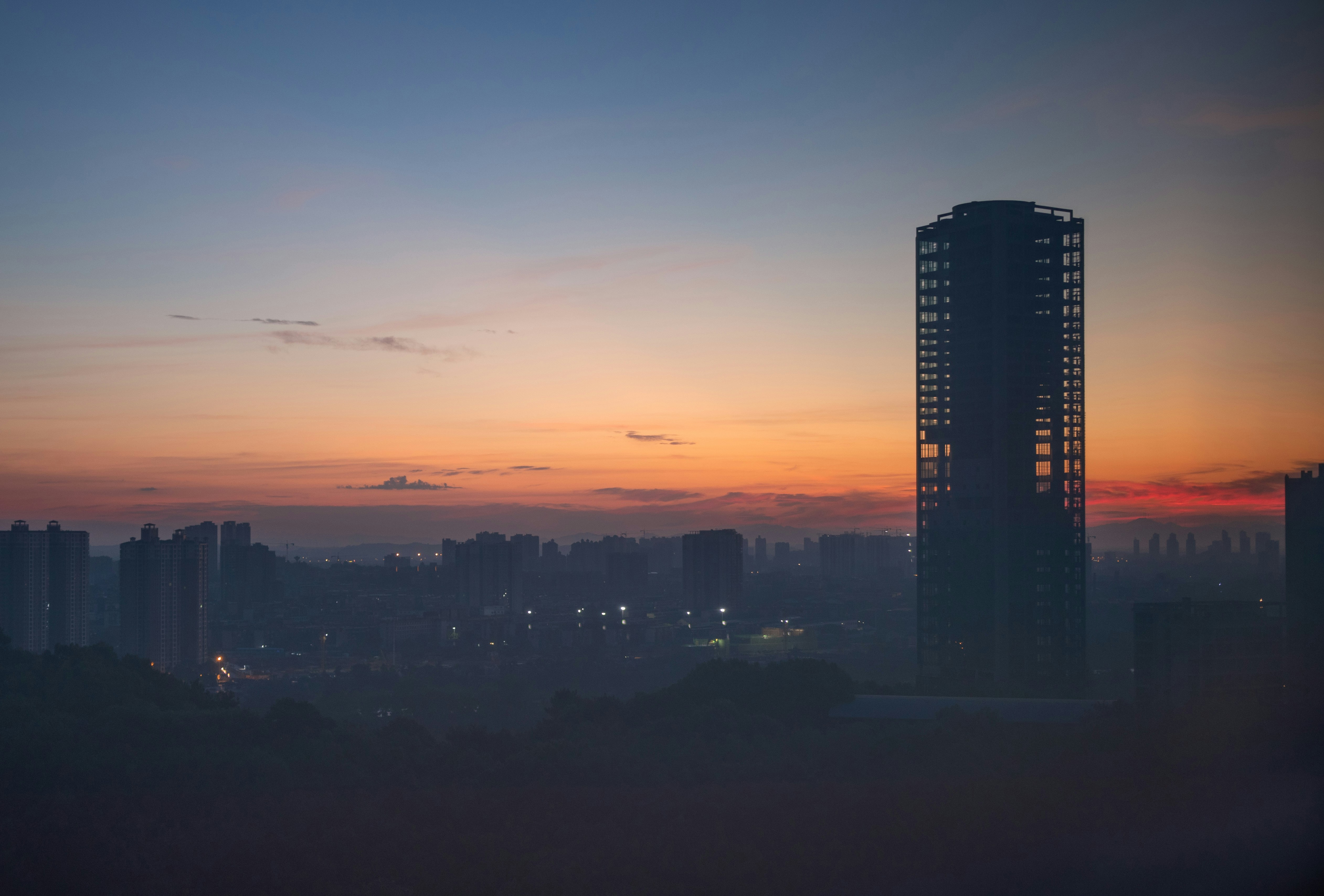 Silhouette of city skyscrapers set against a vibrant sunset with deep orange and blue hues.