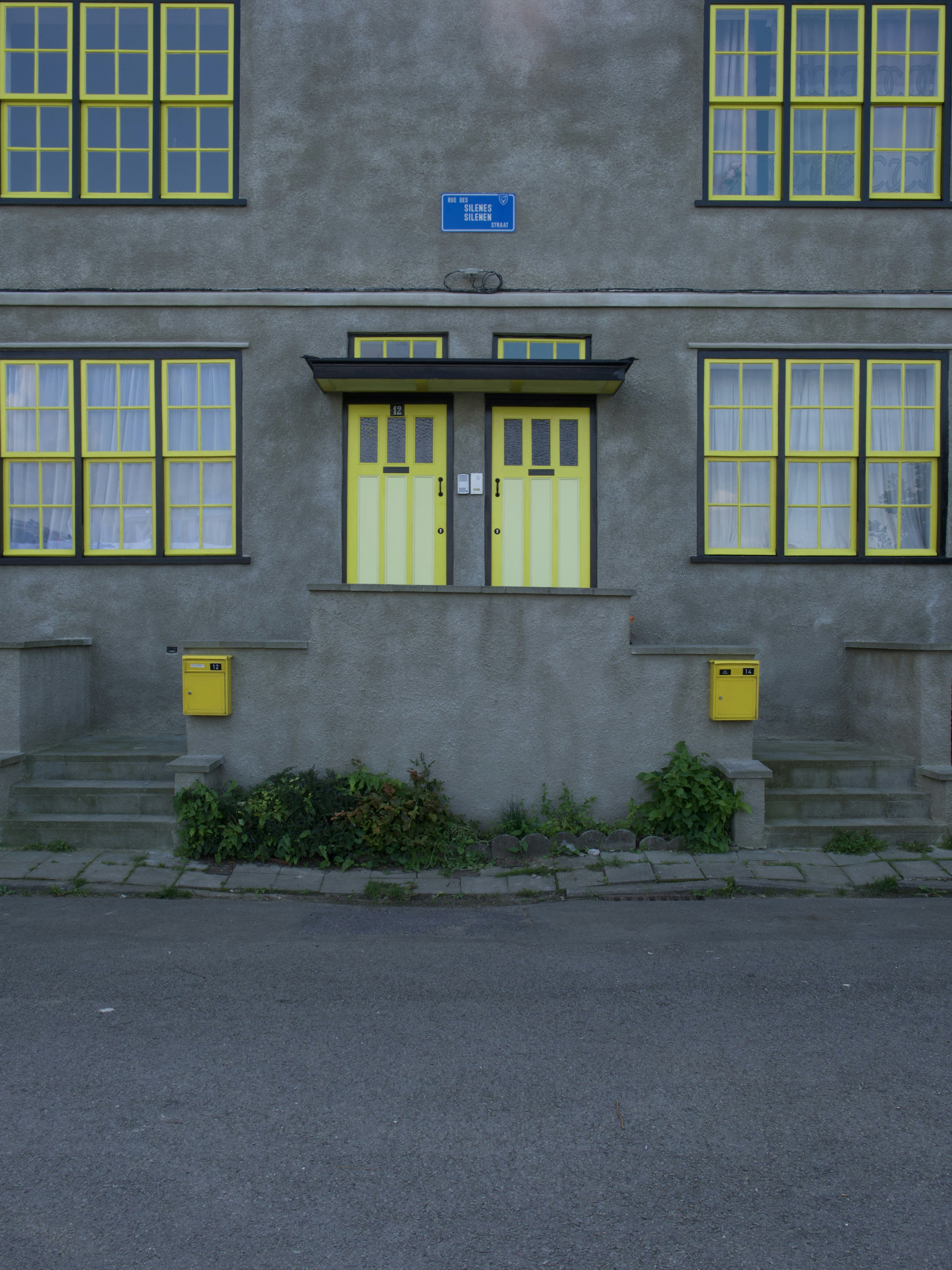 A charming facade featuring two bright yellow doors flanked by large windows, accented by matching mailboxes. The muted gray wall adds contrast to the vibrant colors.