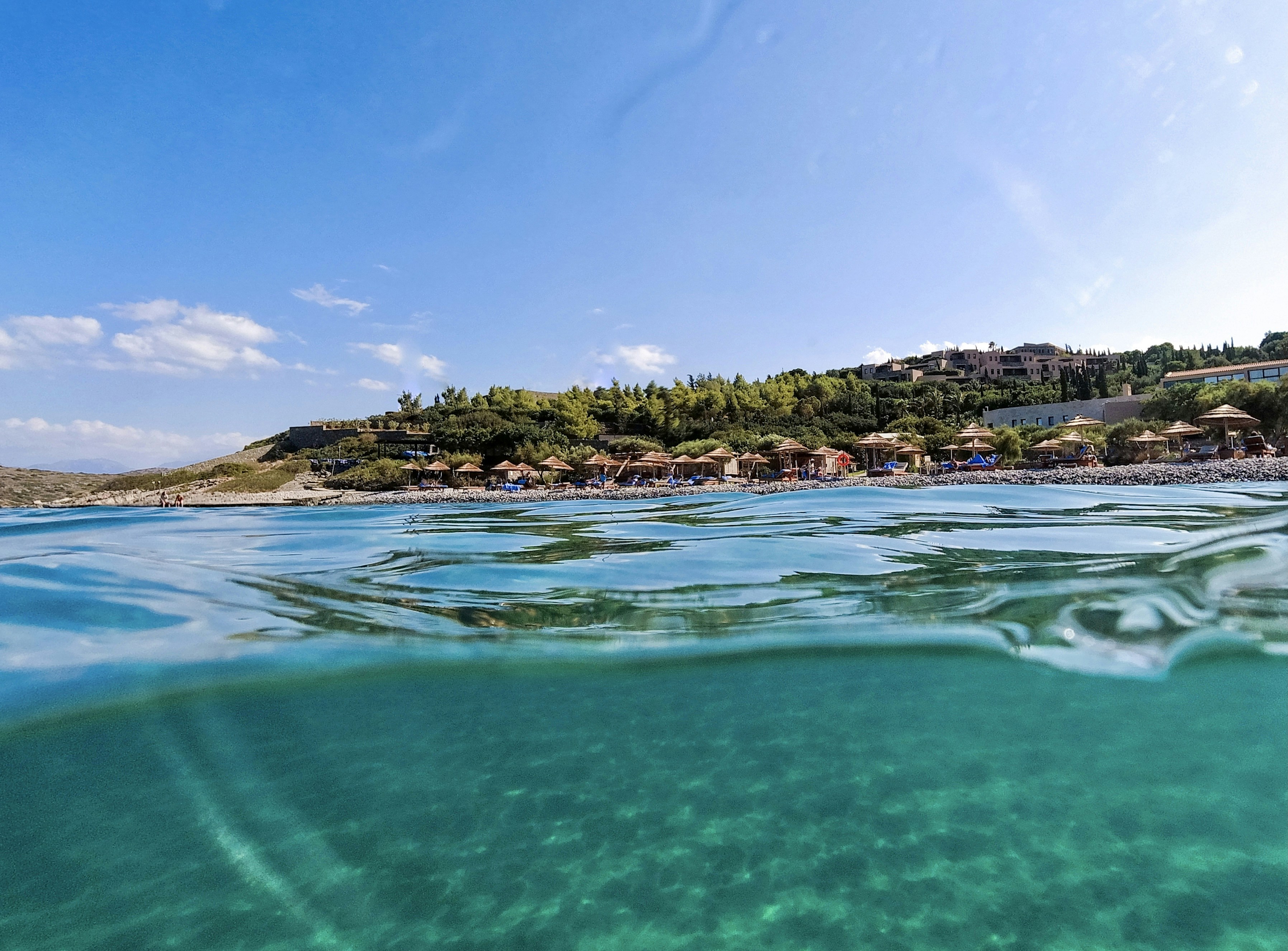 Crystal-clear waters blending with a coastal resort, showcasing a tranquil beach scene. The image captures the gentle undulations of the water's surface.