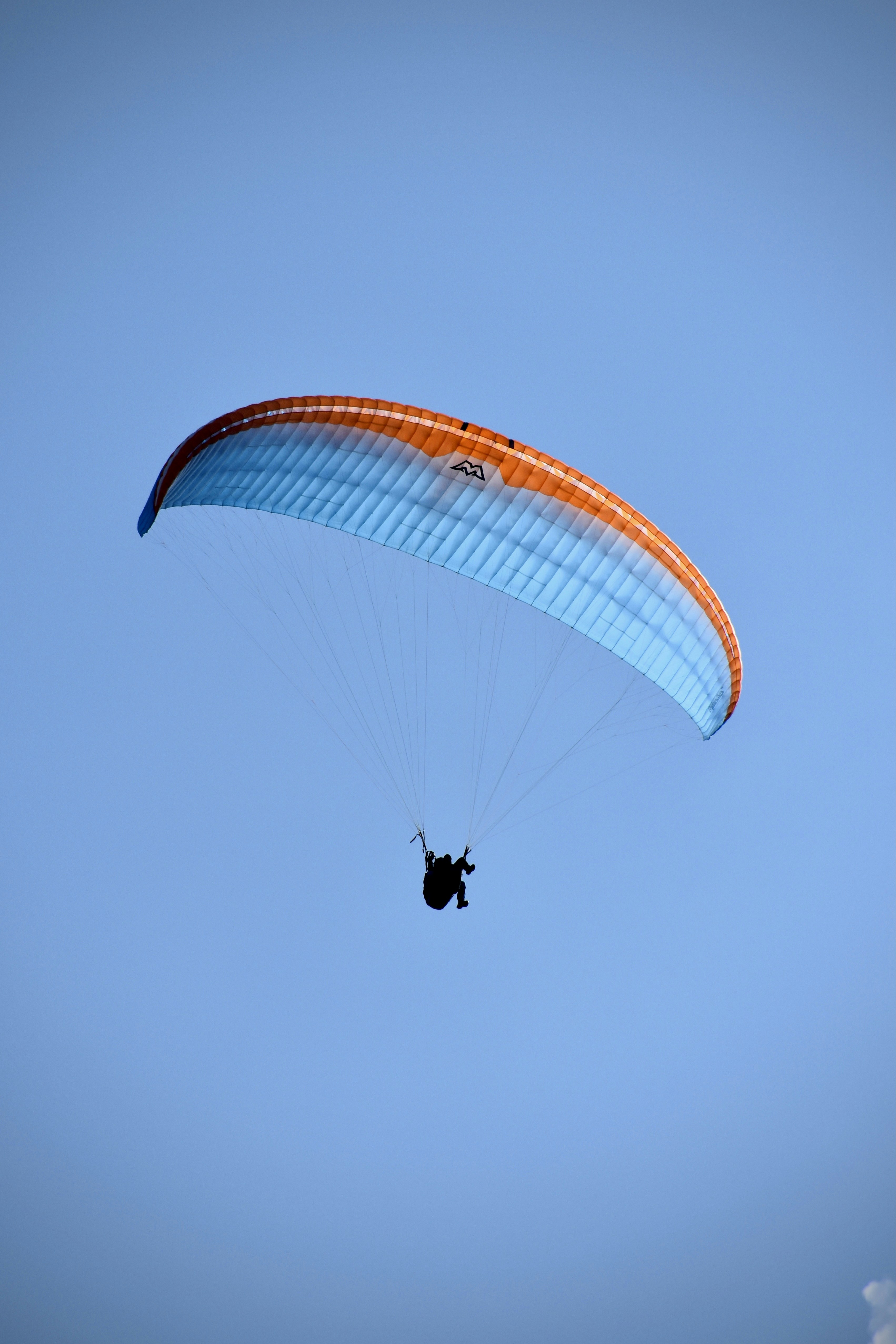 A paraglider gracefully descends against a clear blue sky, showcasing the vibrant colors of the canopy. The scene captures the essence of adventure and tranquility.