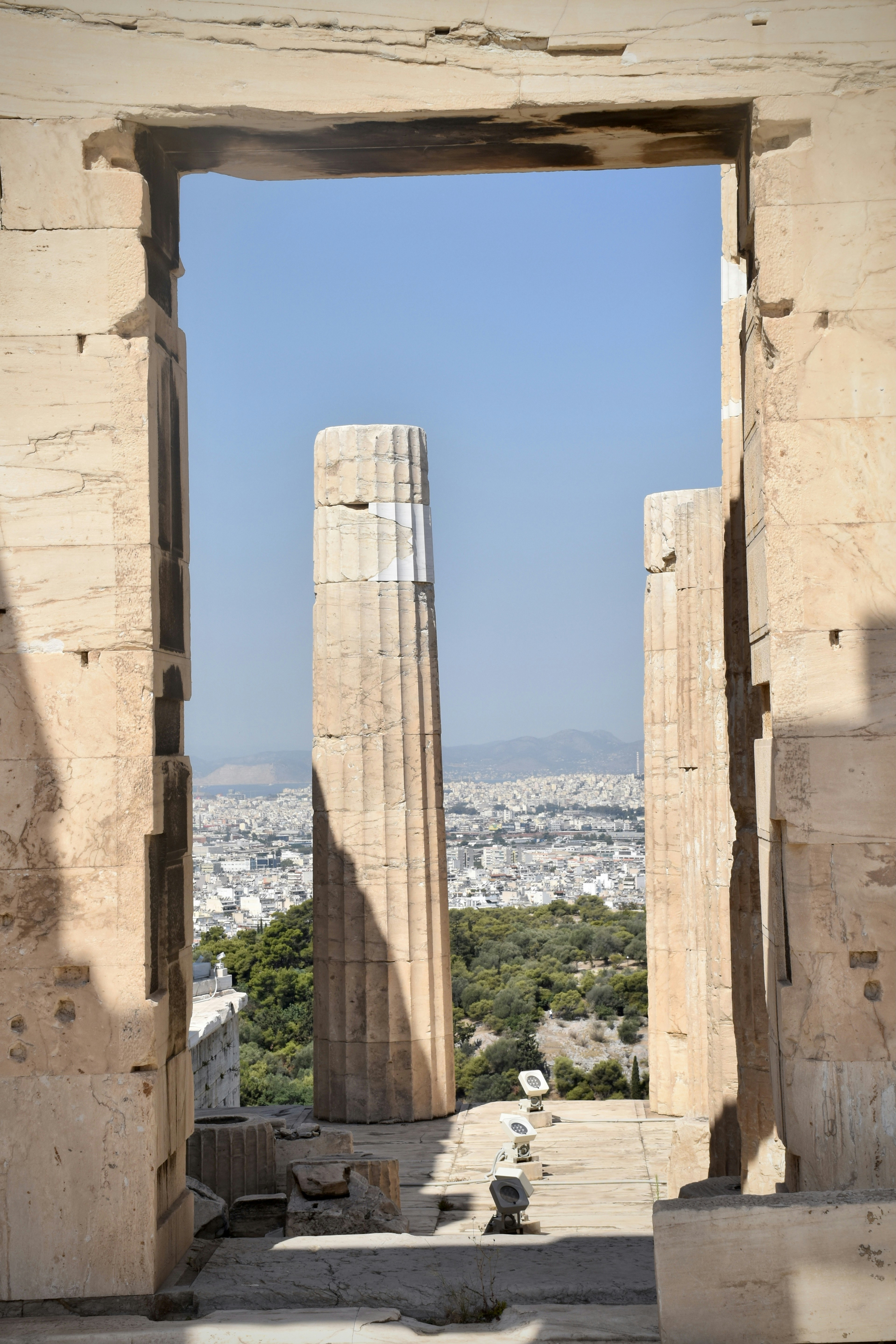 View of ancient columns framed by stone archway, overlooking a modern cityscape in the background.