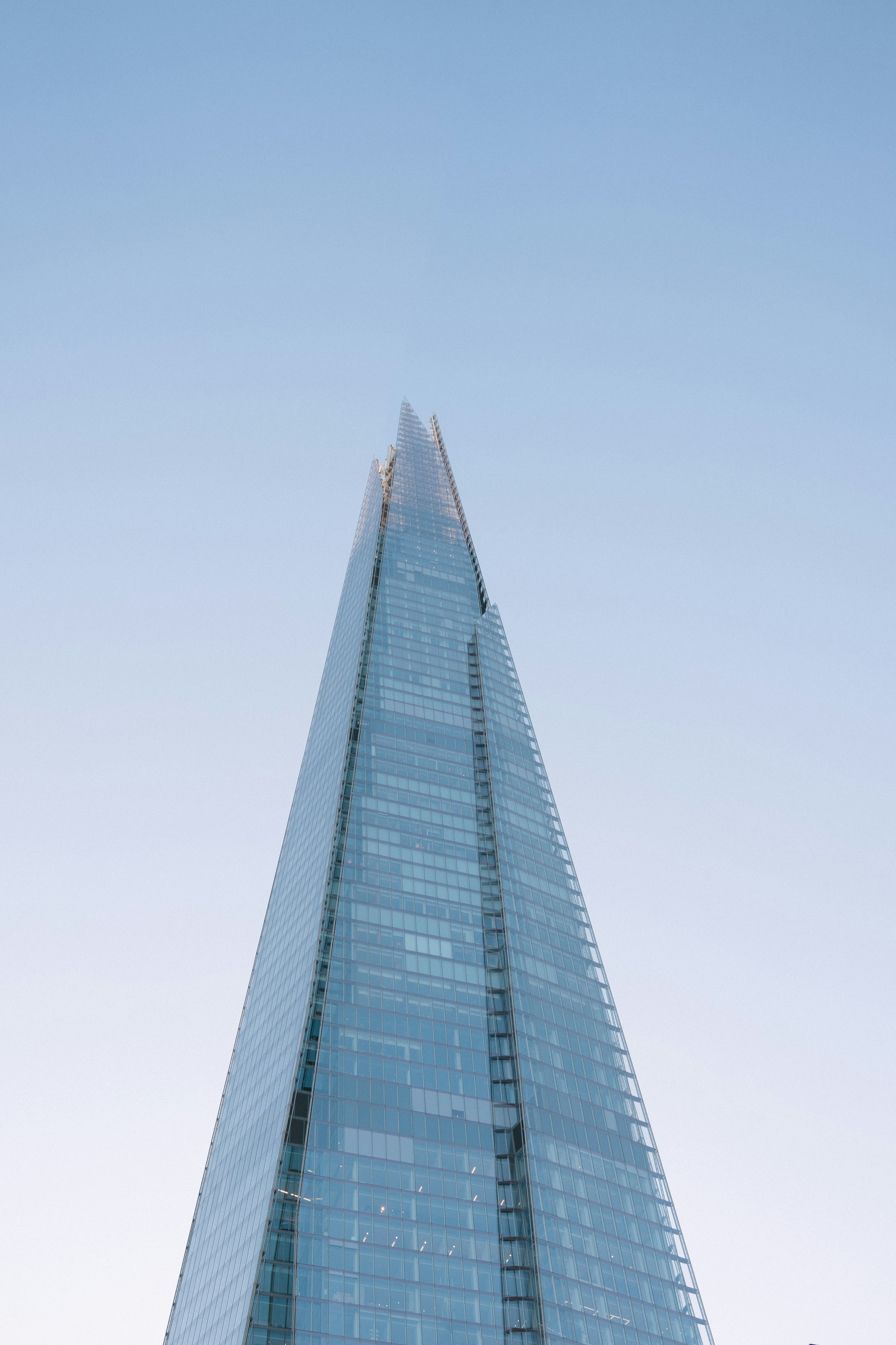 Sleek glass tower reaching skyward against a clear blue backdrop, showcasing contemporary design. The structure’s sharp angles and reflective surfaces highlight its innovative architecture.