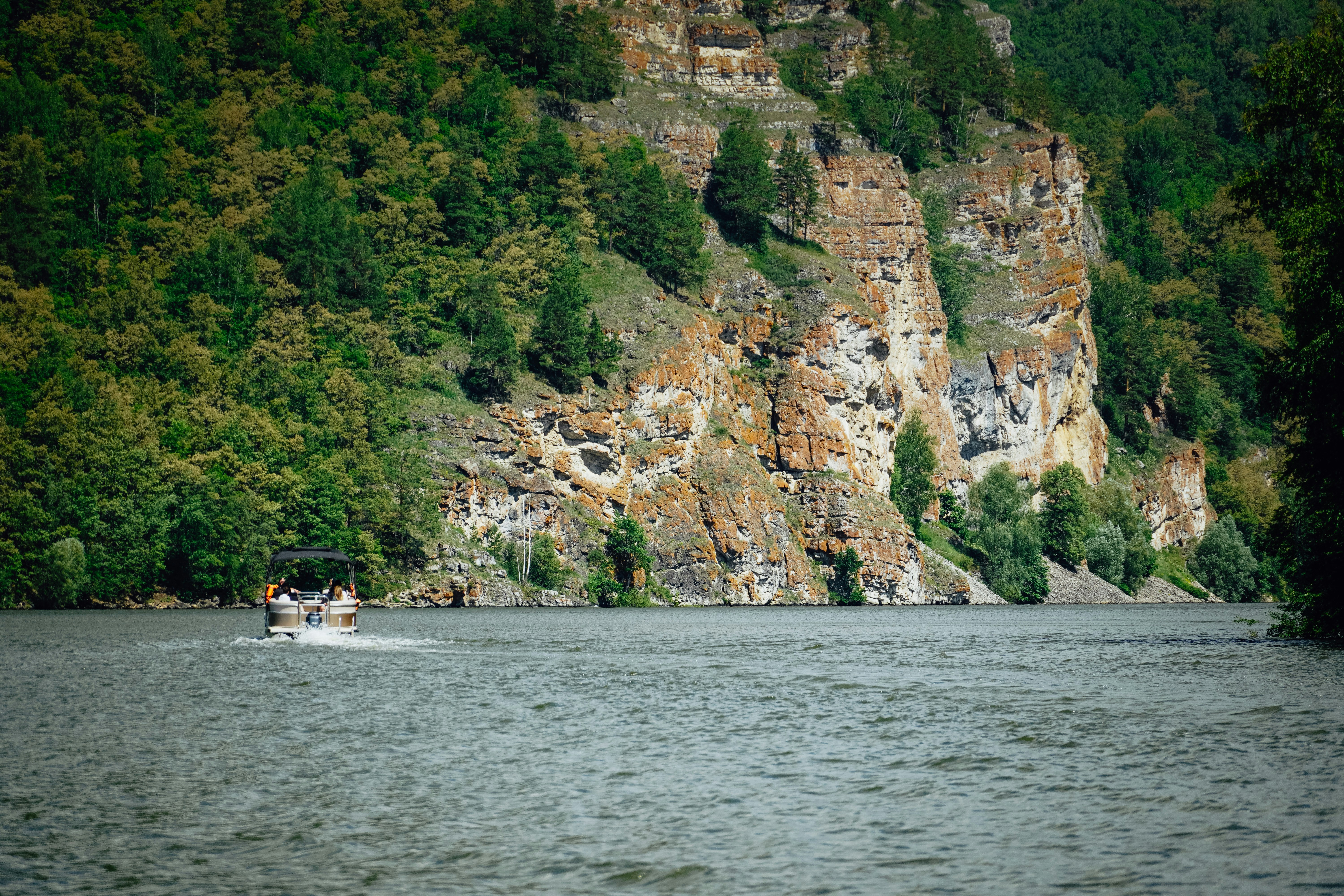 Lone Boat Drifts Past Sunlit Cliff-Lined River