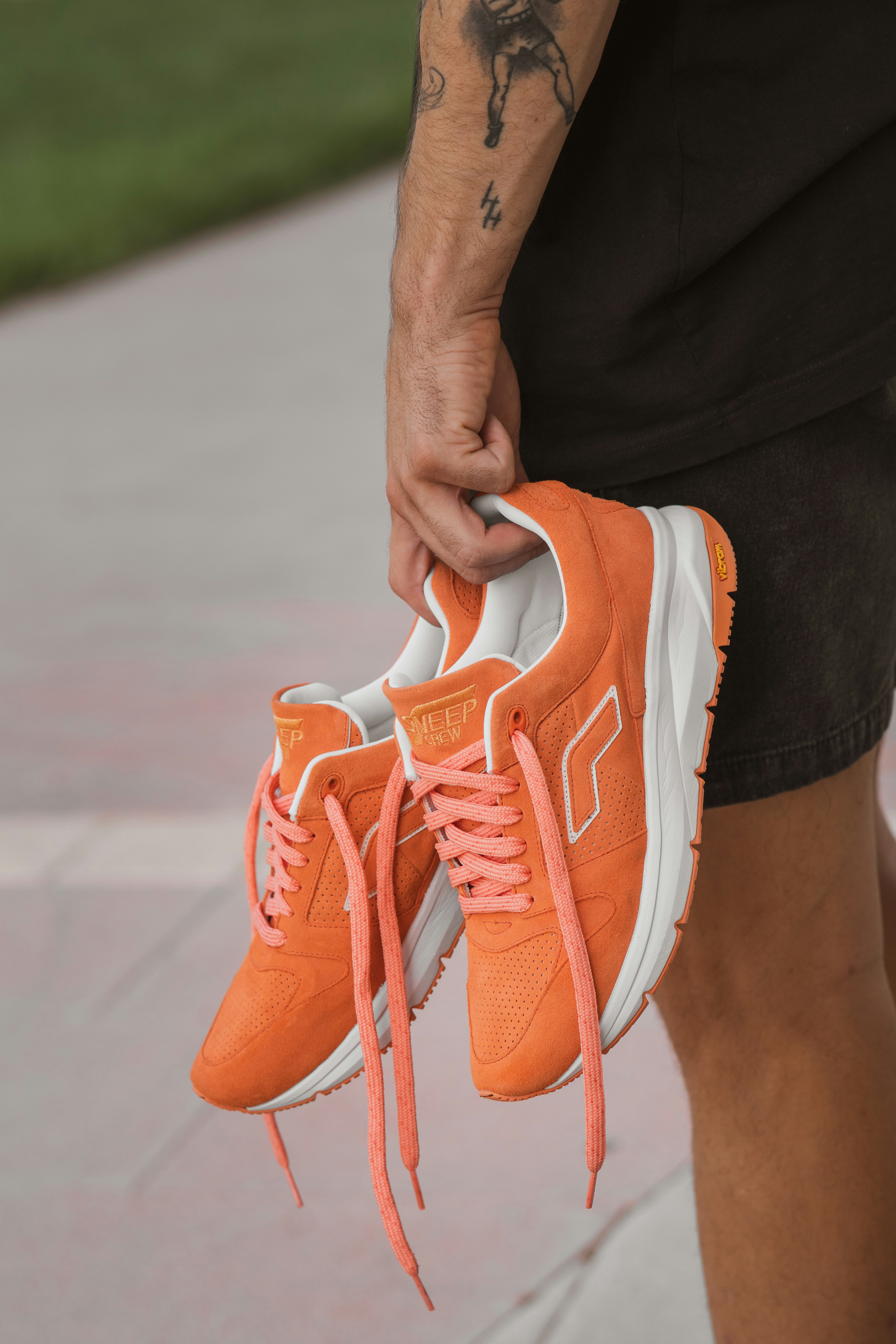 Bright Orange Sneakers Dangled in Hand with Shaded Leg