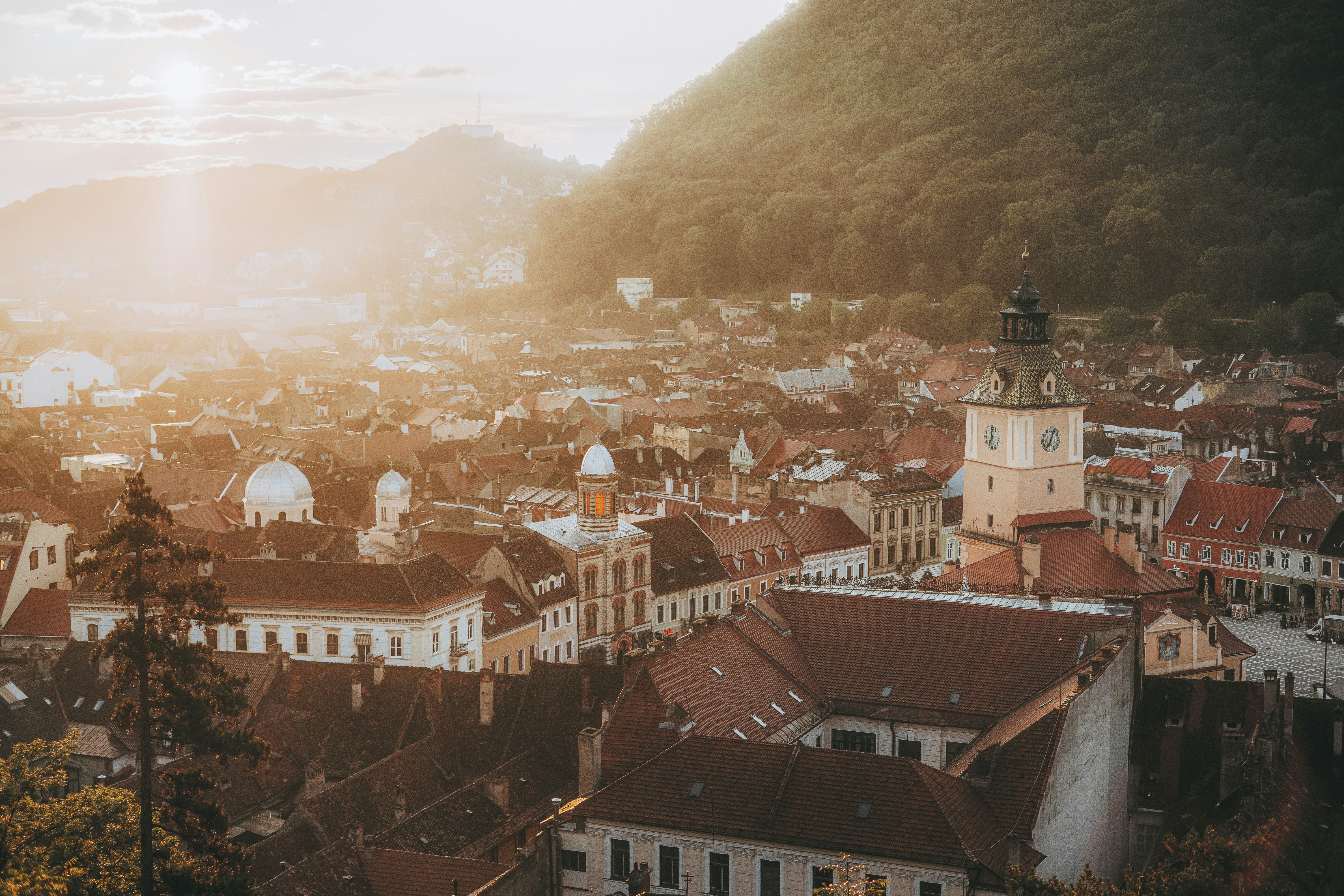 Sunset light bathes a historic town's rooftops with a mountain in the background.