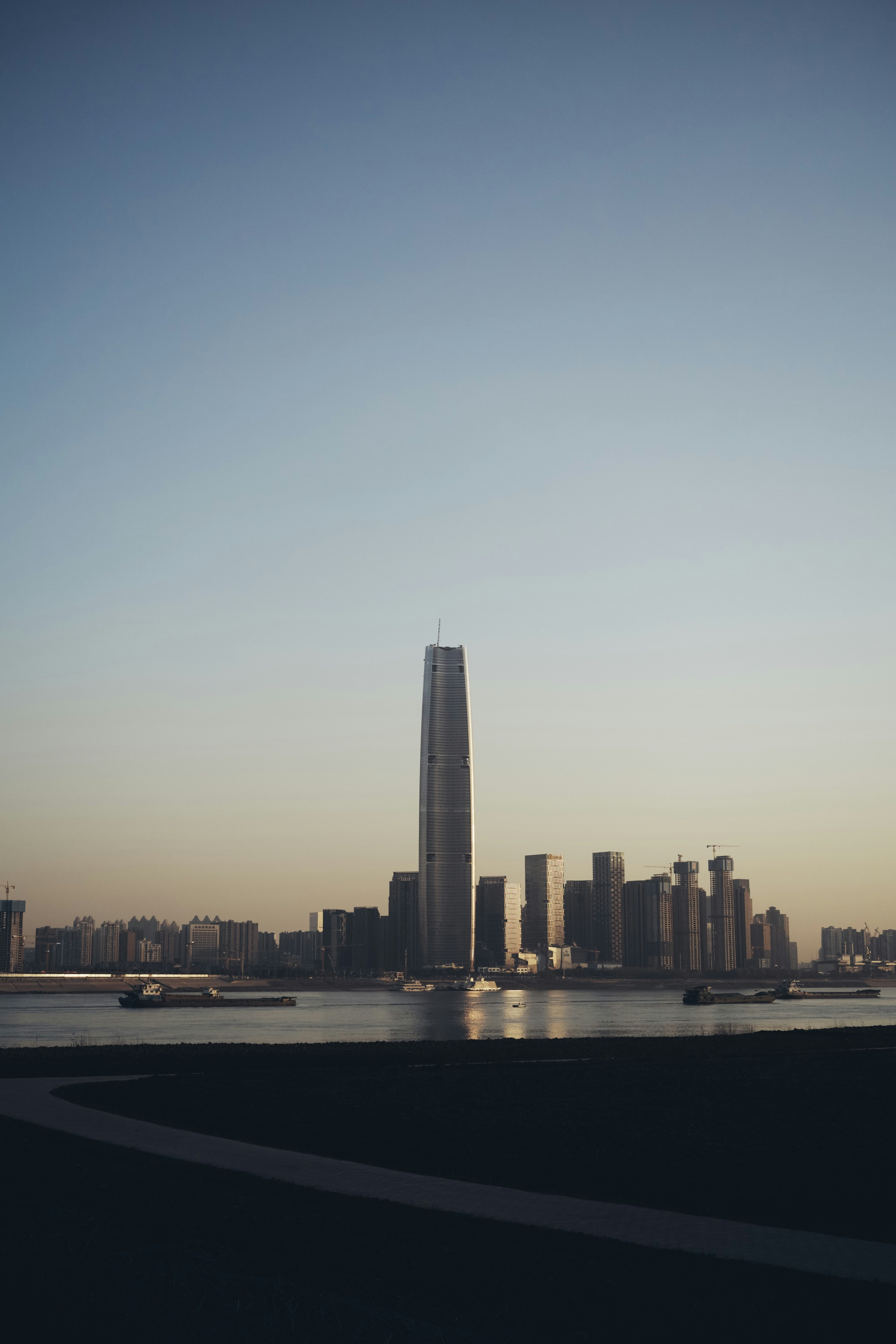 A towering skyscraper stands prominently against a softly lit skyline, reflecting on the water below. The architectural lines contrast beautifully with the fading light.
