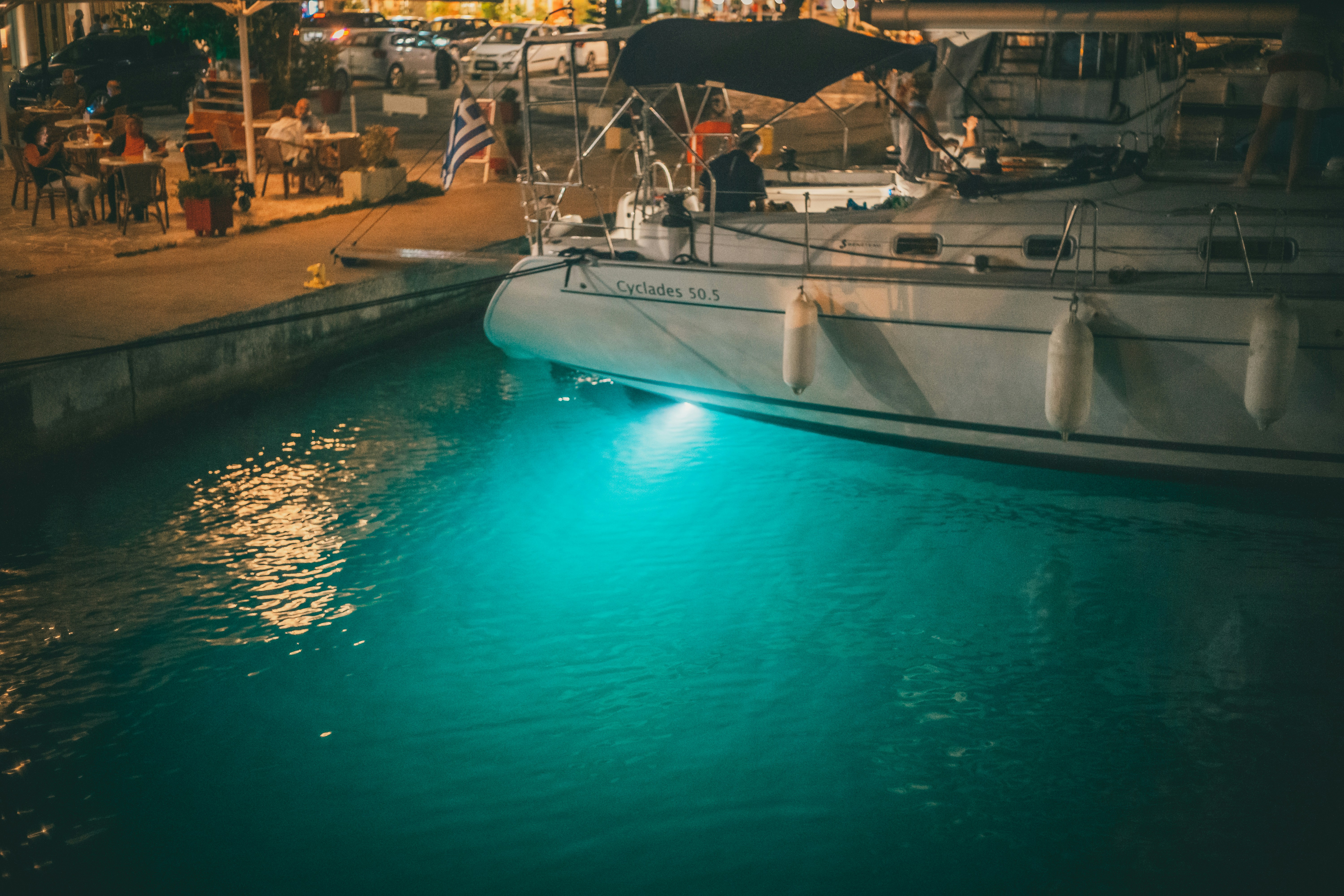 A catamaran illuminated by soft underwater lights, anchored in tranquil waters at night, surrounded by a vibrant harbor ambiance.