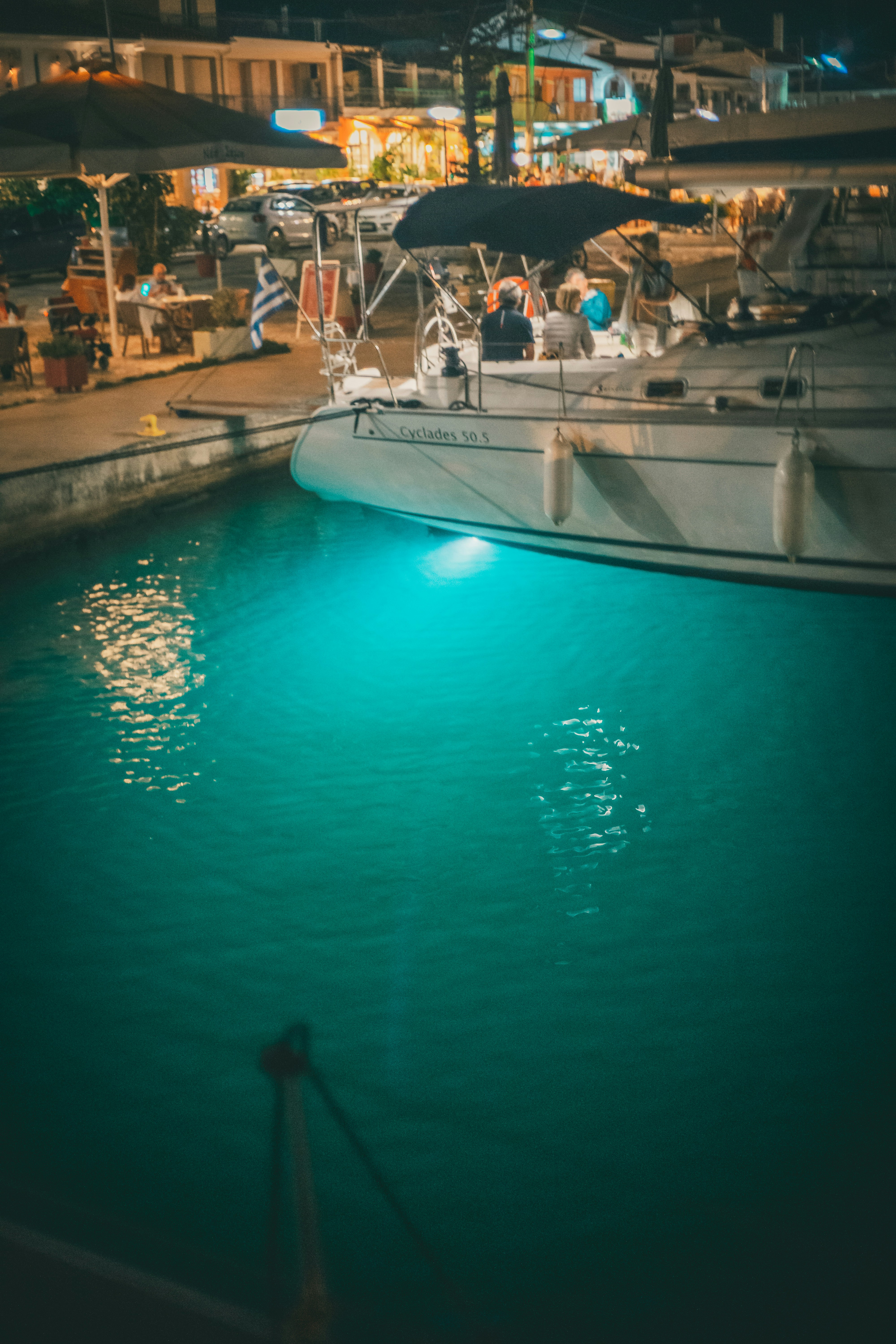 Teal Reflections at a Night Marina: Sailboat Docked Under Warm Lights