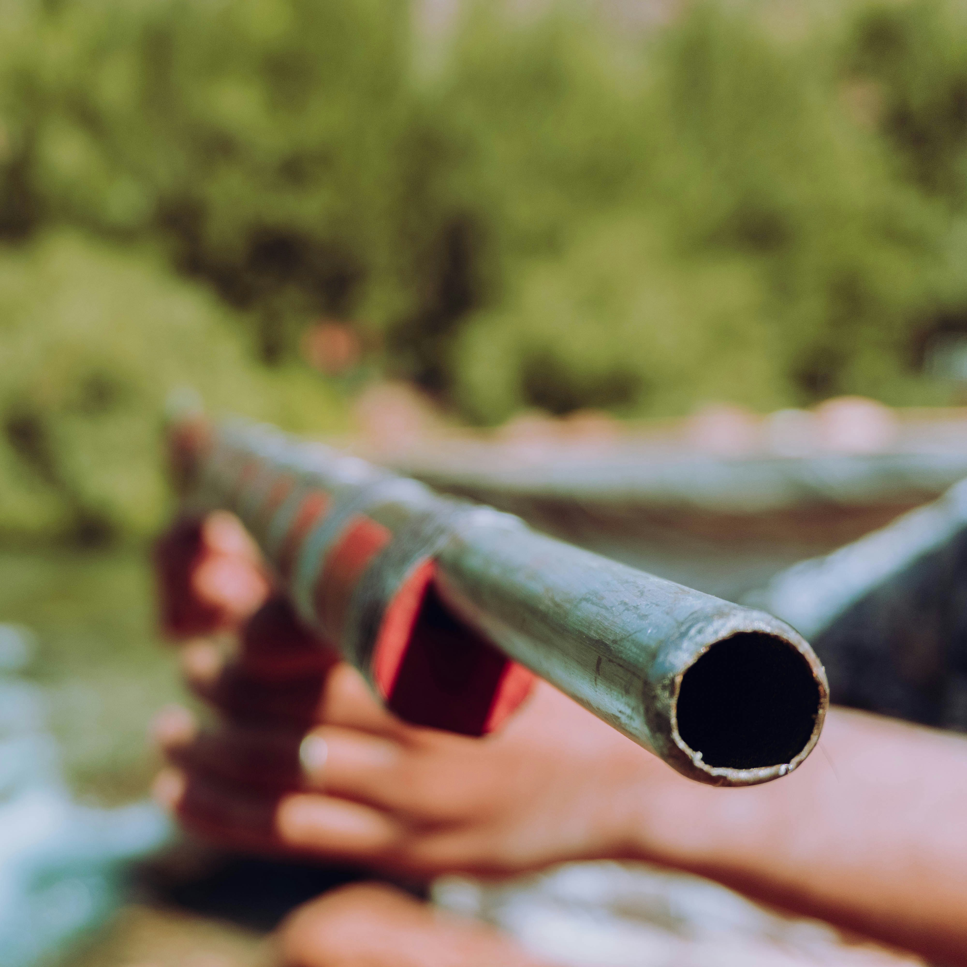 A Hand-Held Green Pipe Reaches Toward a Quiet Riverside